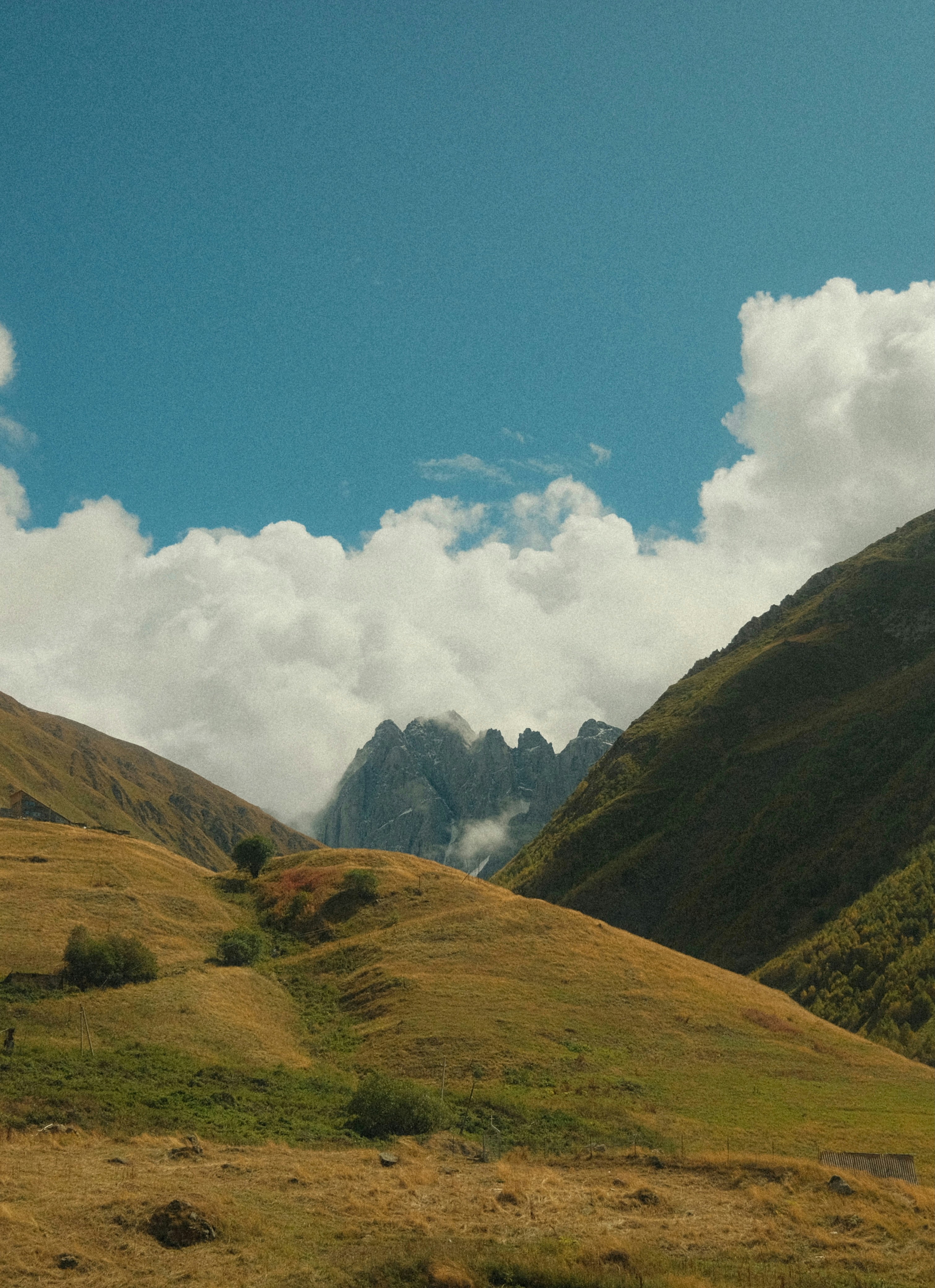 Majestic mountain range framed by lush hills under a dramatic sky filled with clouds.