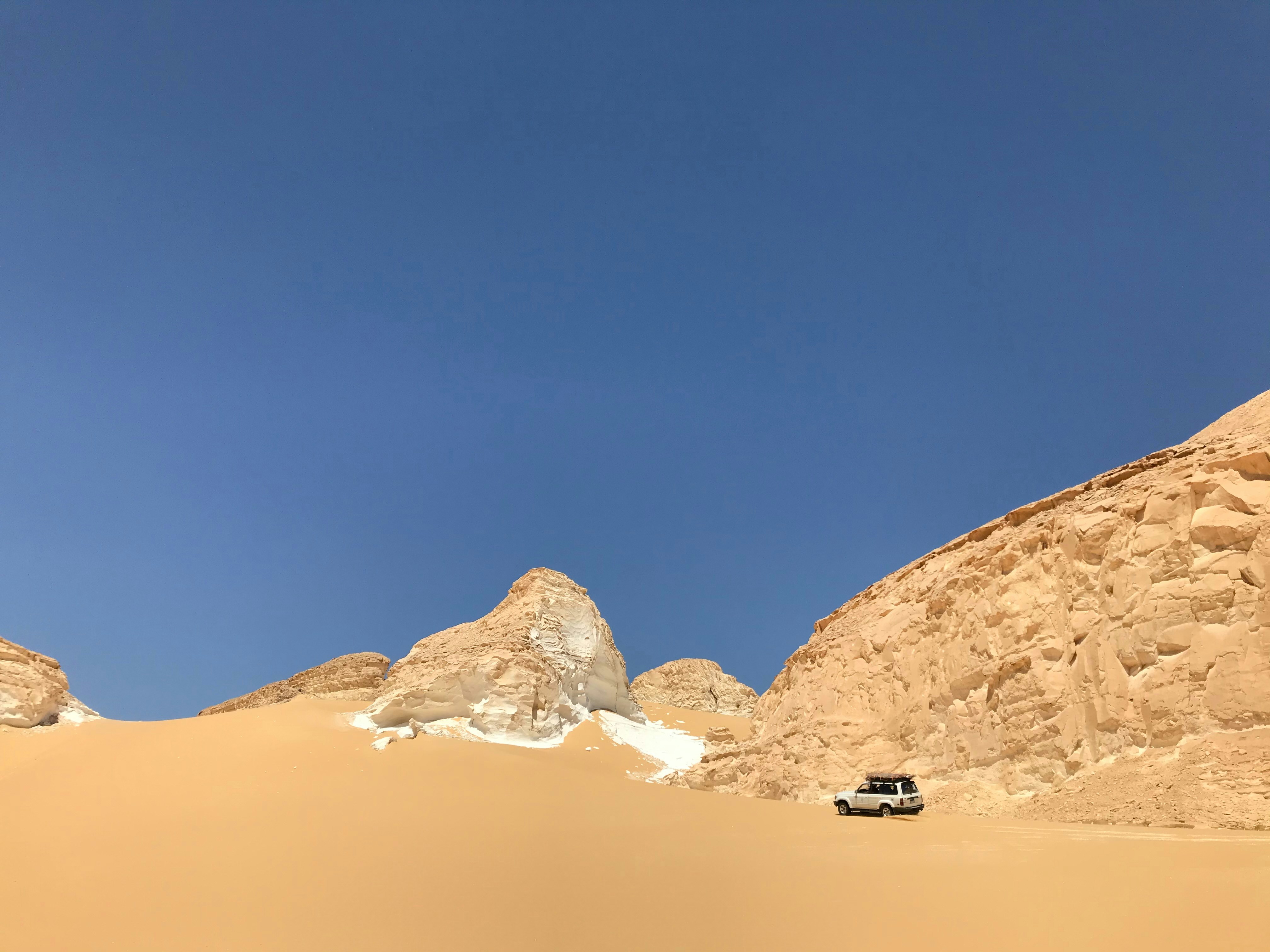 A white jeep drives through a desert landscape.