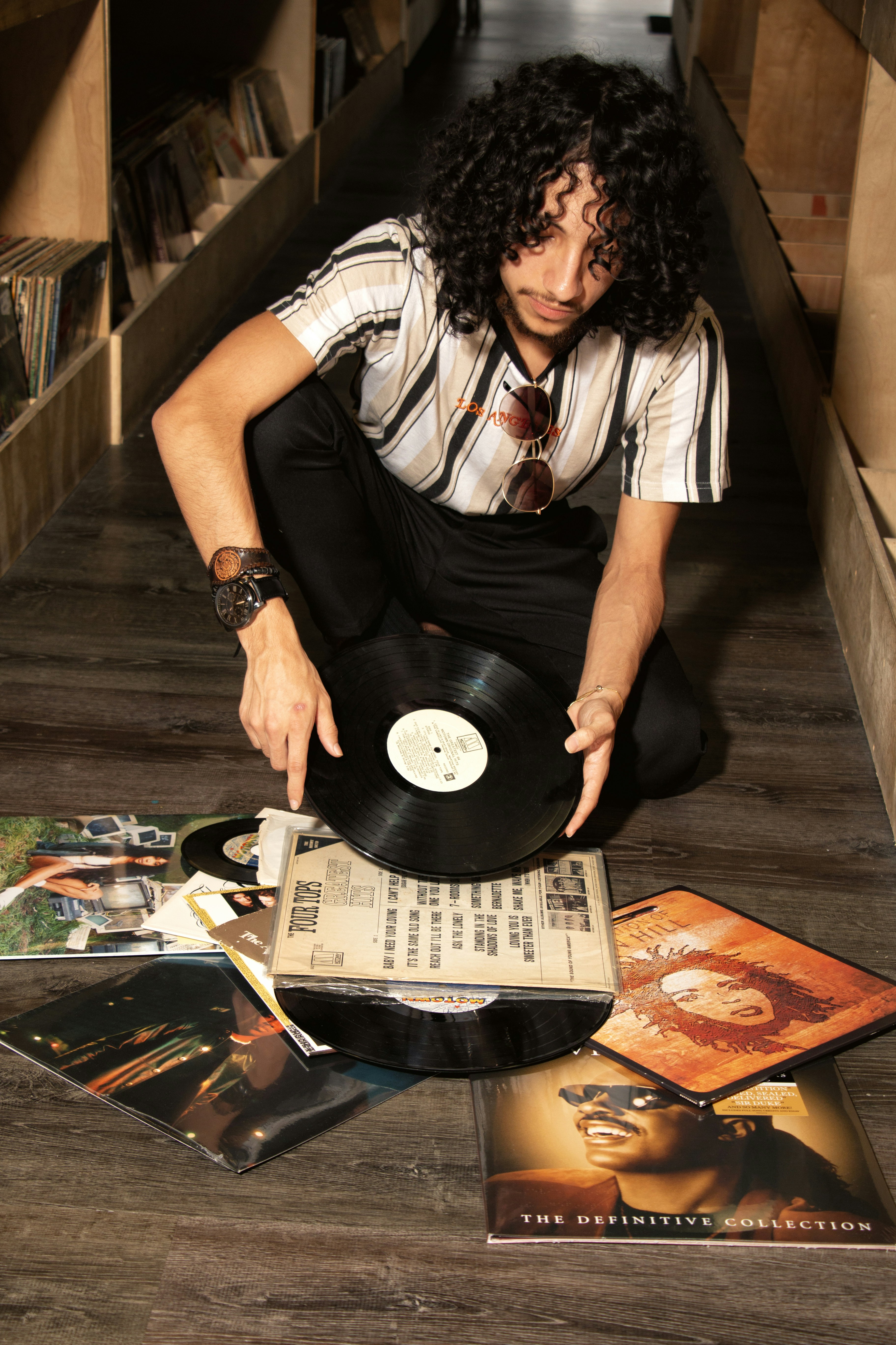 Young man exploring a collection of vinyl records on the floor, showcasing a blend of music nostalgia and personal style.