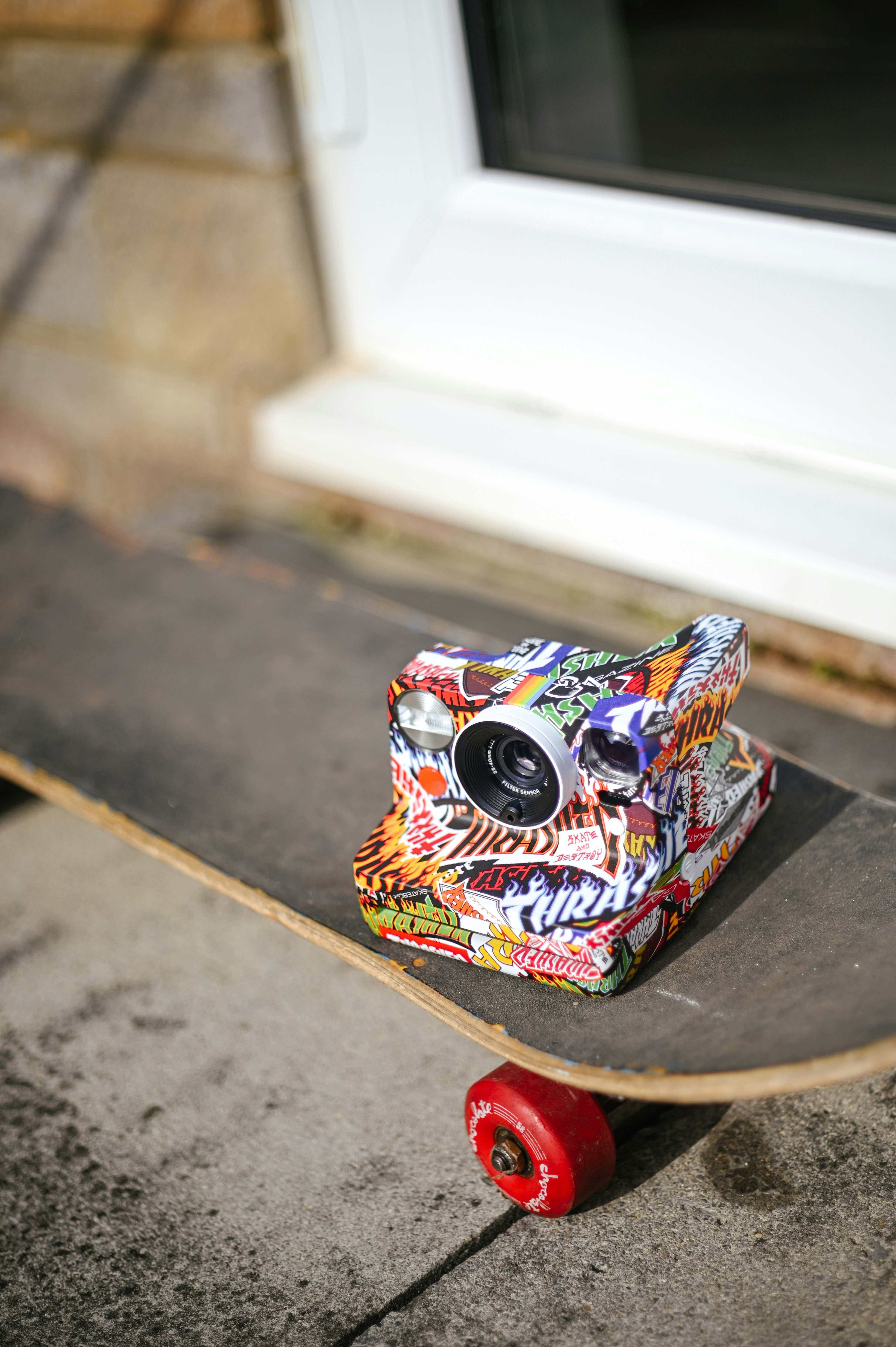 Graffiti-wrapped camera perched on a tiny skateboard by a bright doorway