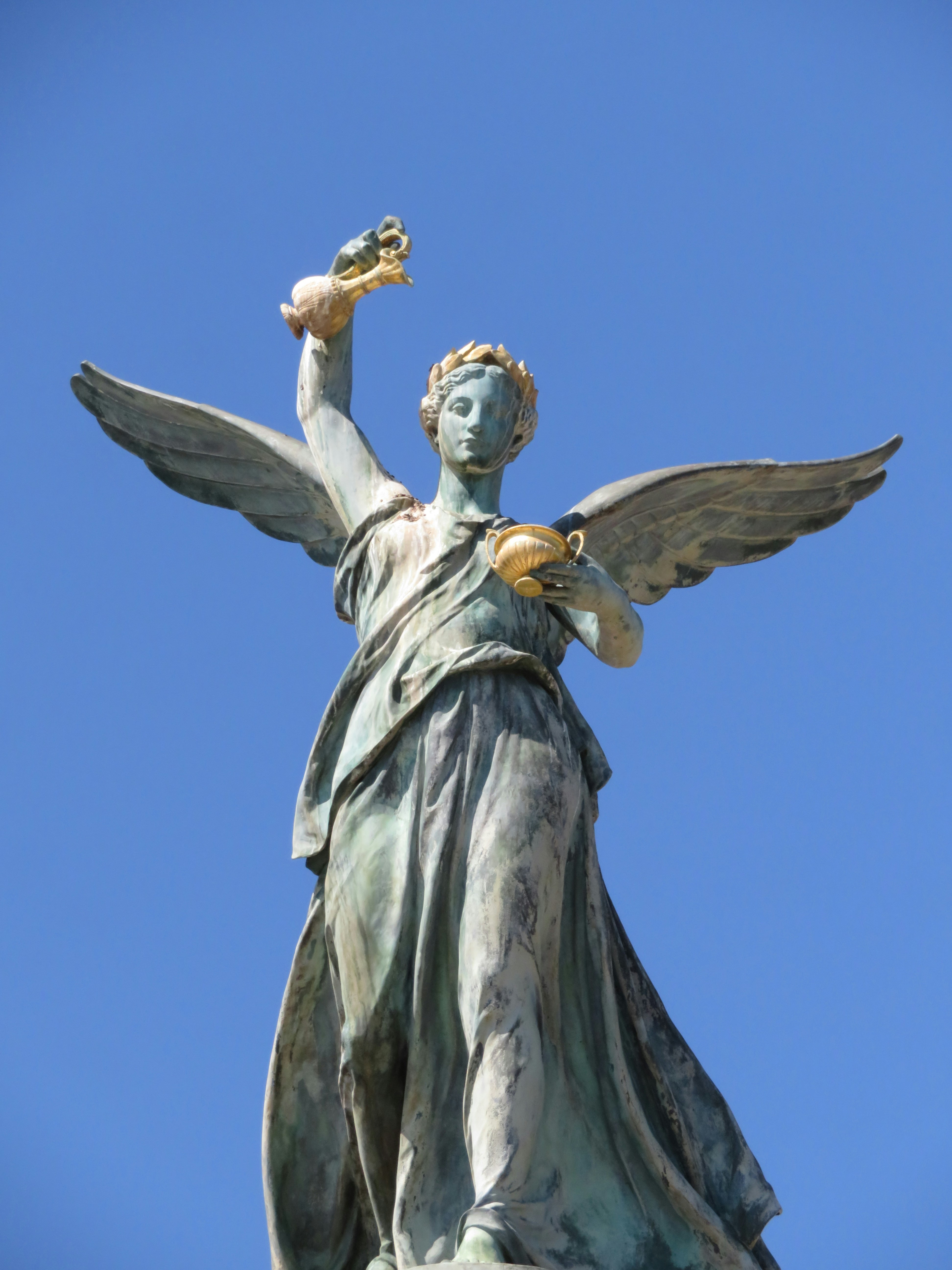 Winged statue holding wreath against blue sky