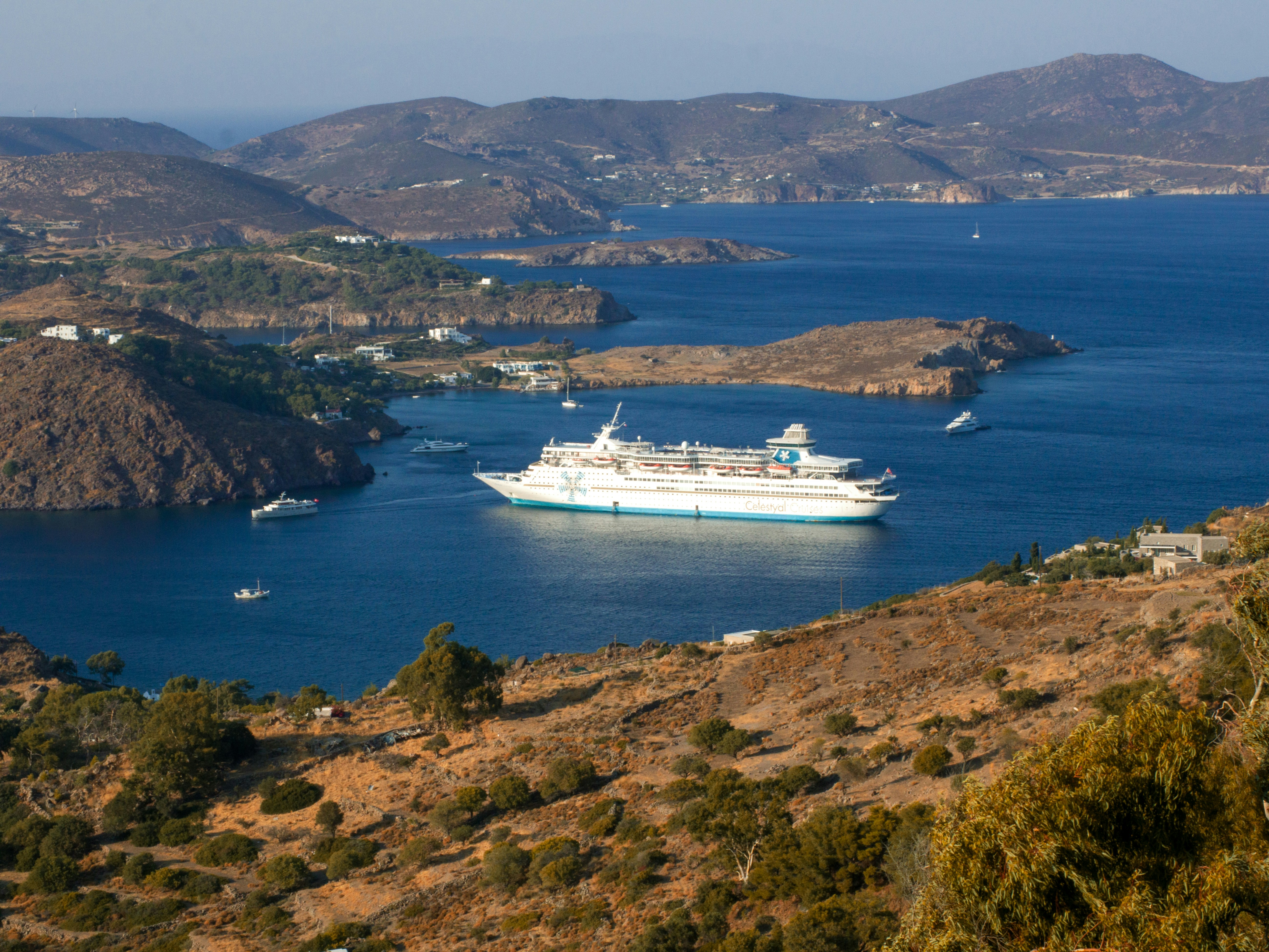 A cruise ship anchored in a tranquil bay surrounded by rugged hills and clear blue waters, illustrating the harmony between nature and maritime travel.
