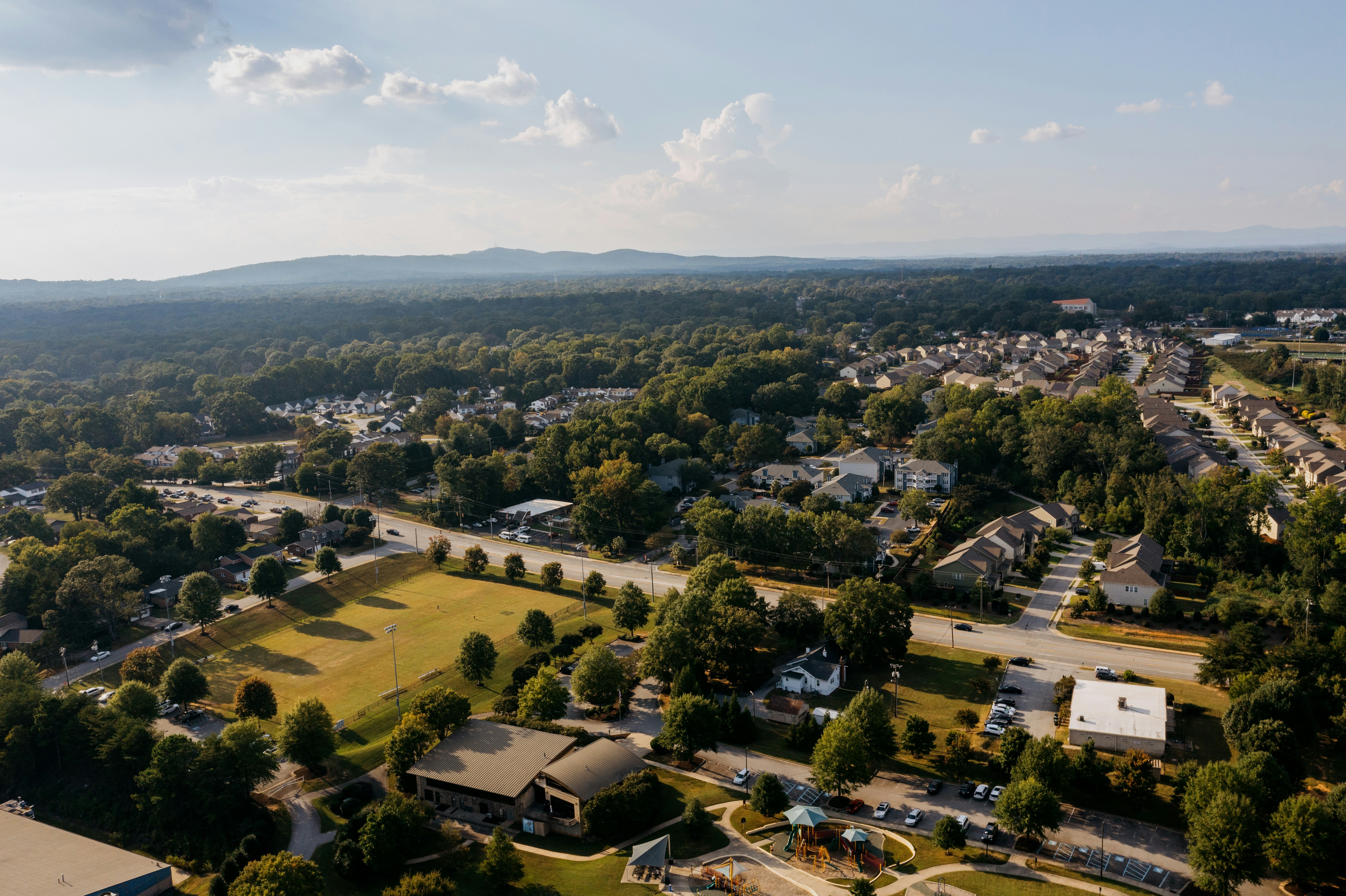 Expansive view of a suburban landscape showcasing neatly arranged homes, lush greenery, and winding roads under a clear sky.