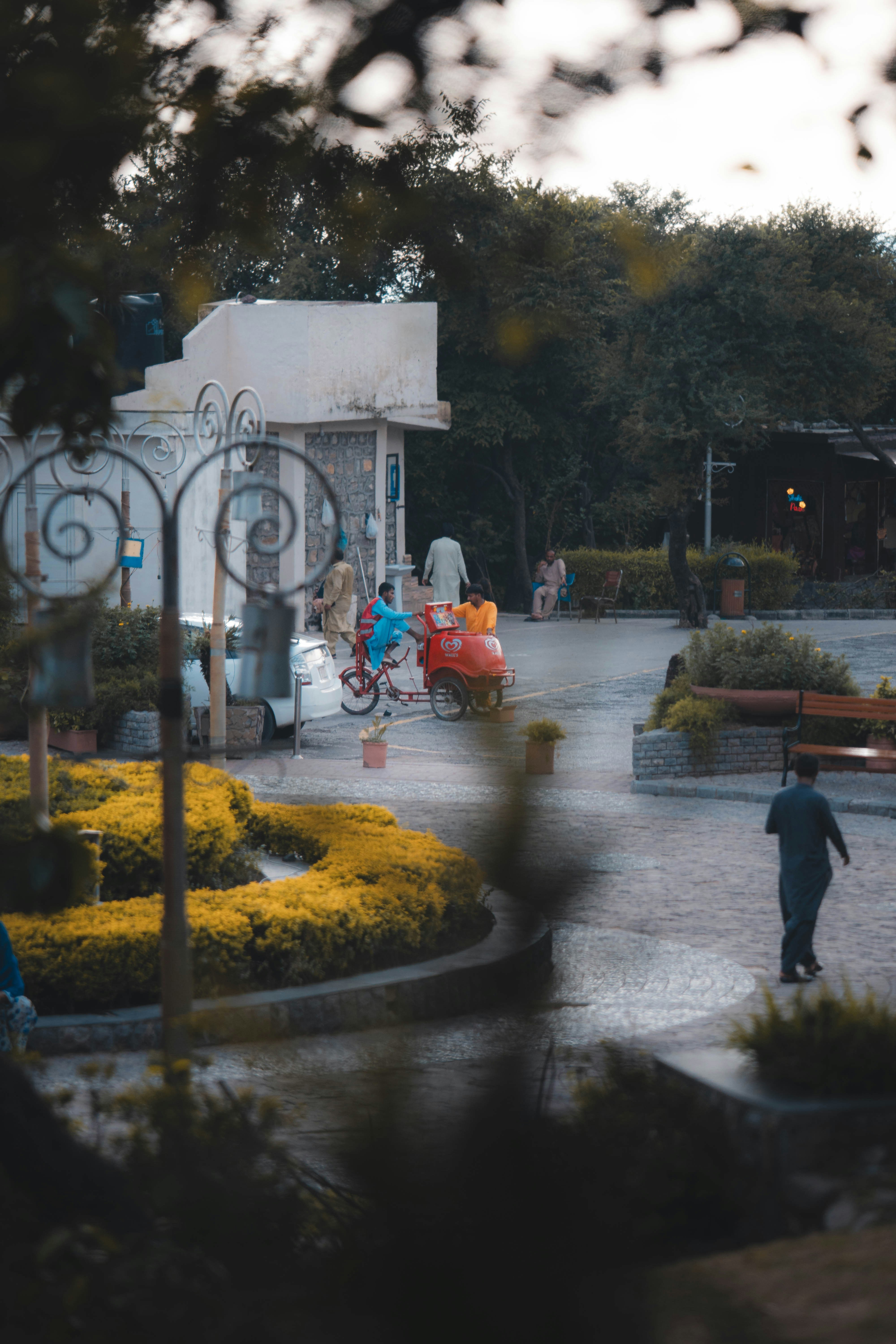 Sunlit Plaza Convergence: White kiosk, iron arches, and a red cart