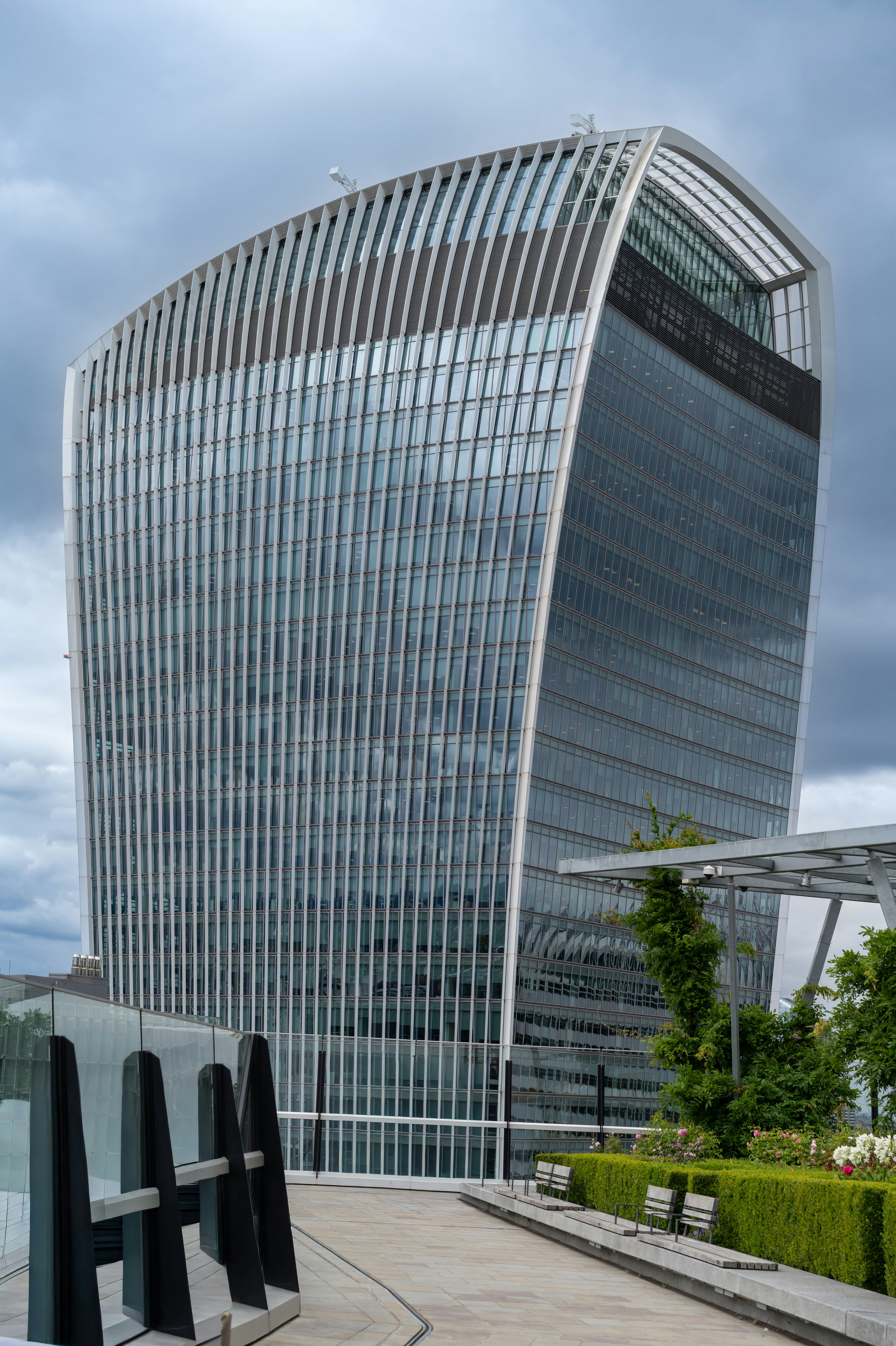 Sleek skyscraper with a unique curved design reflecting the sky, surrounded by greenery and urban elements.
