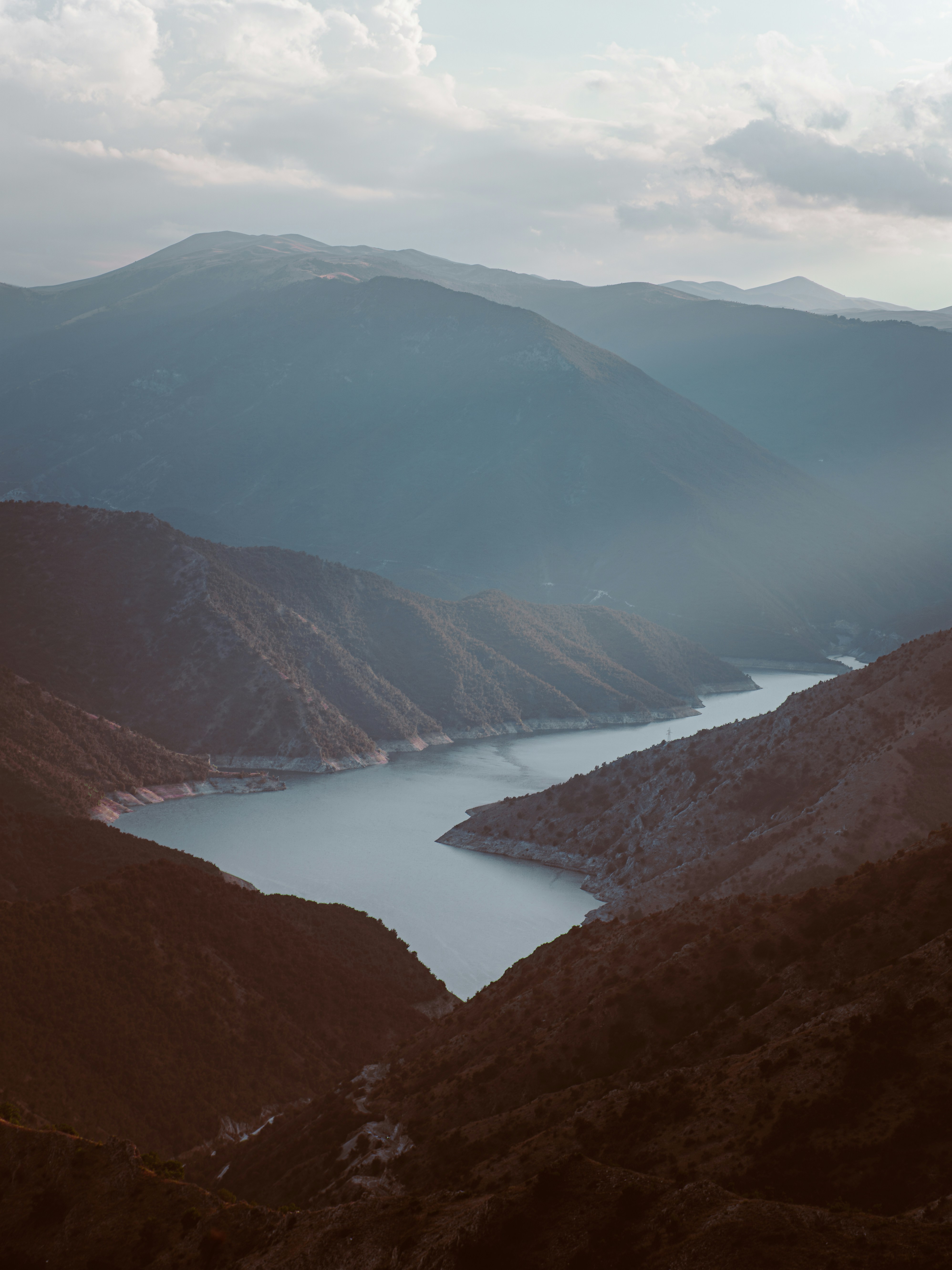 A serene lake winds through misty mountain valleys.
