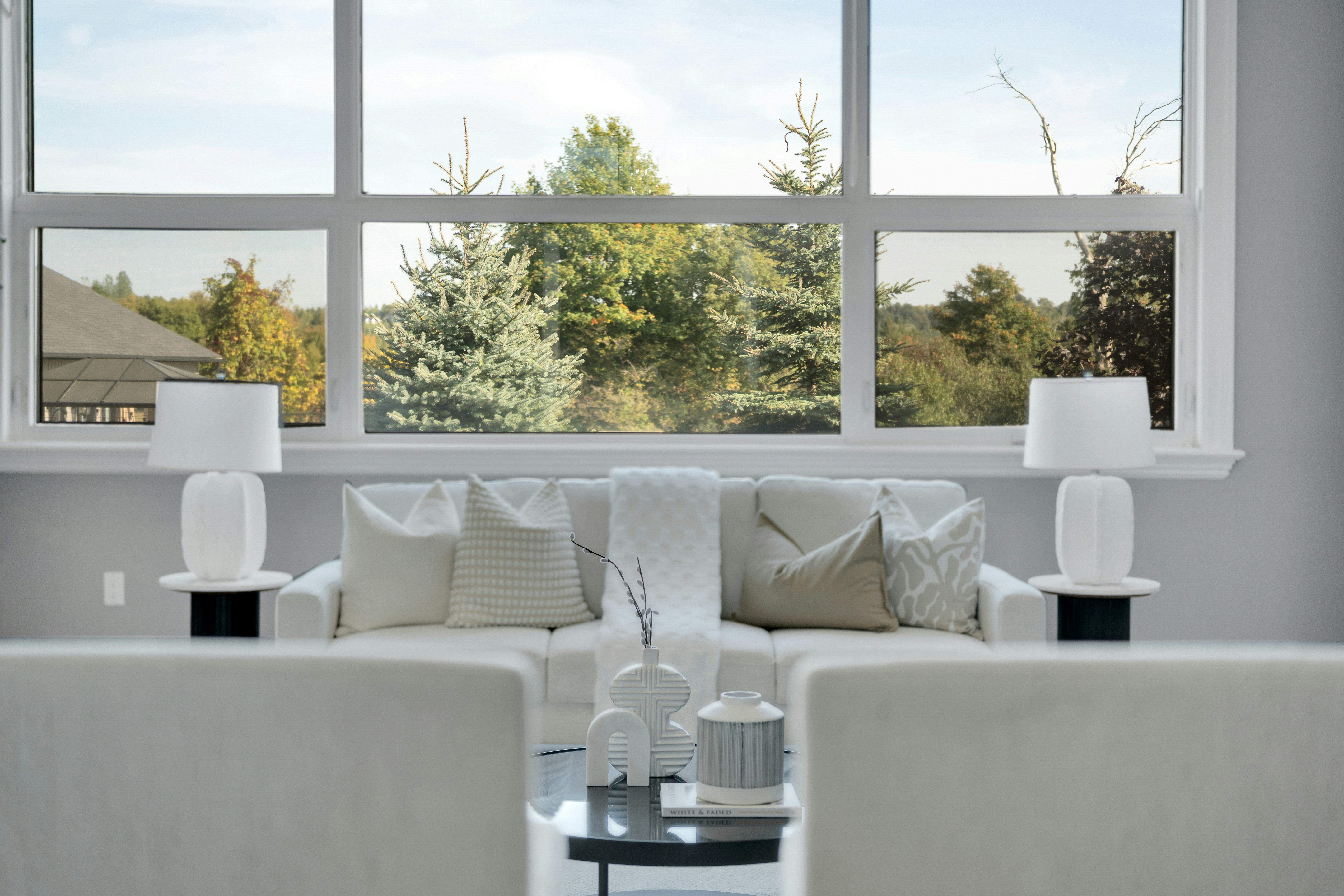 Modern living room featuring a cozy sofa and decorative elements, framed by large windows showcasing lush greenery outside.