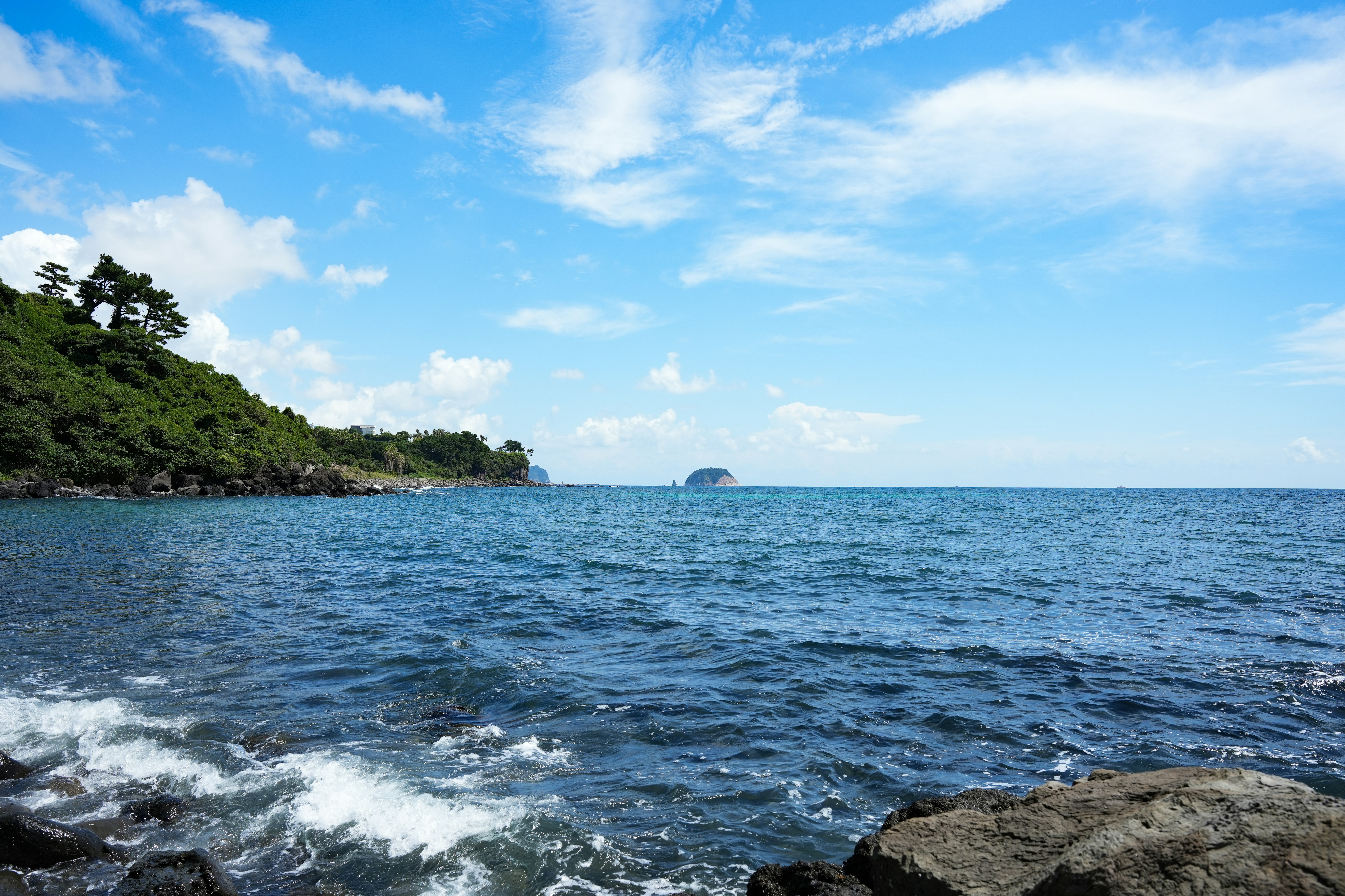 Blue ocean with rocky shore and distant island.