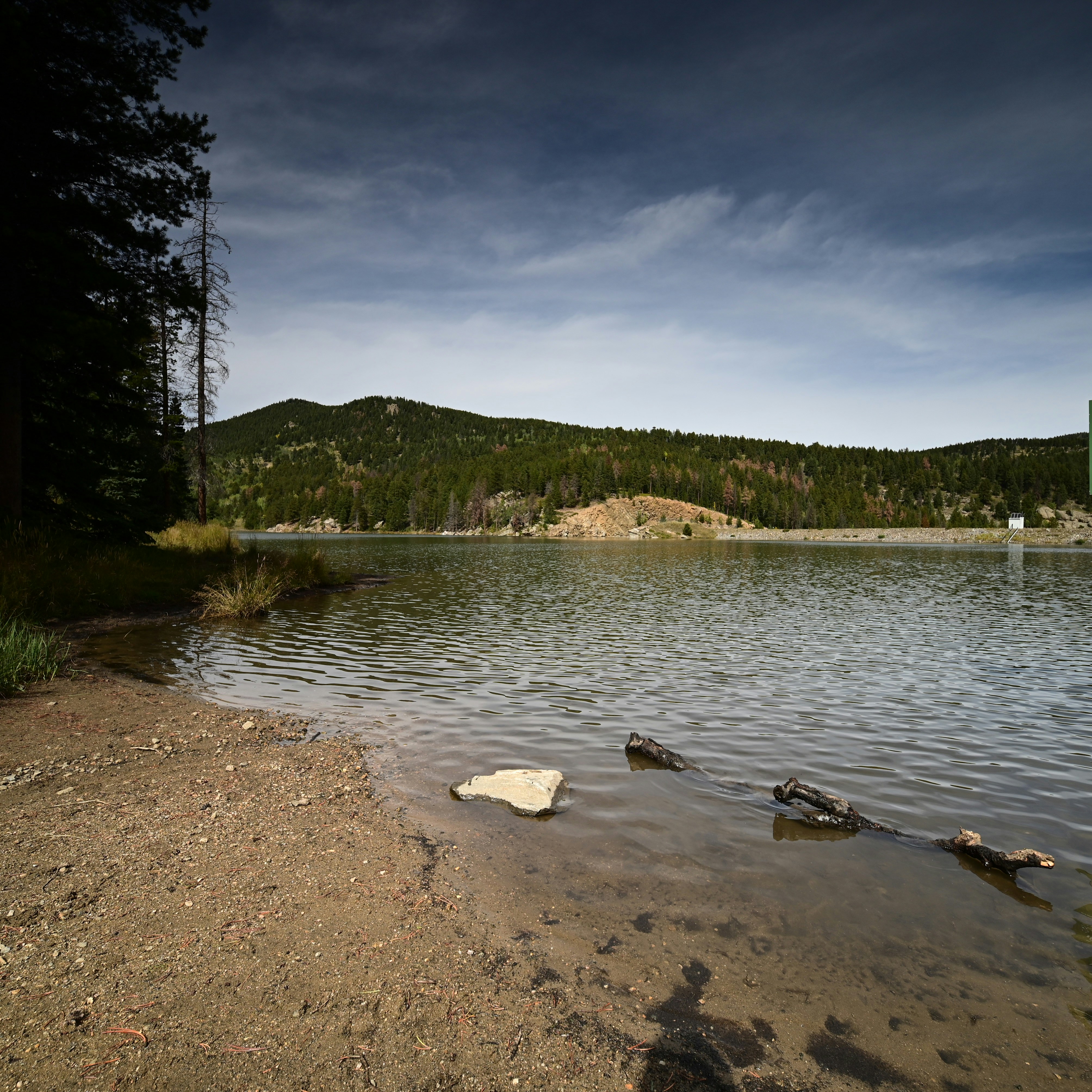 Calm lake with trees and mountains under cloudy sky.