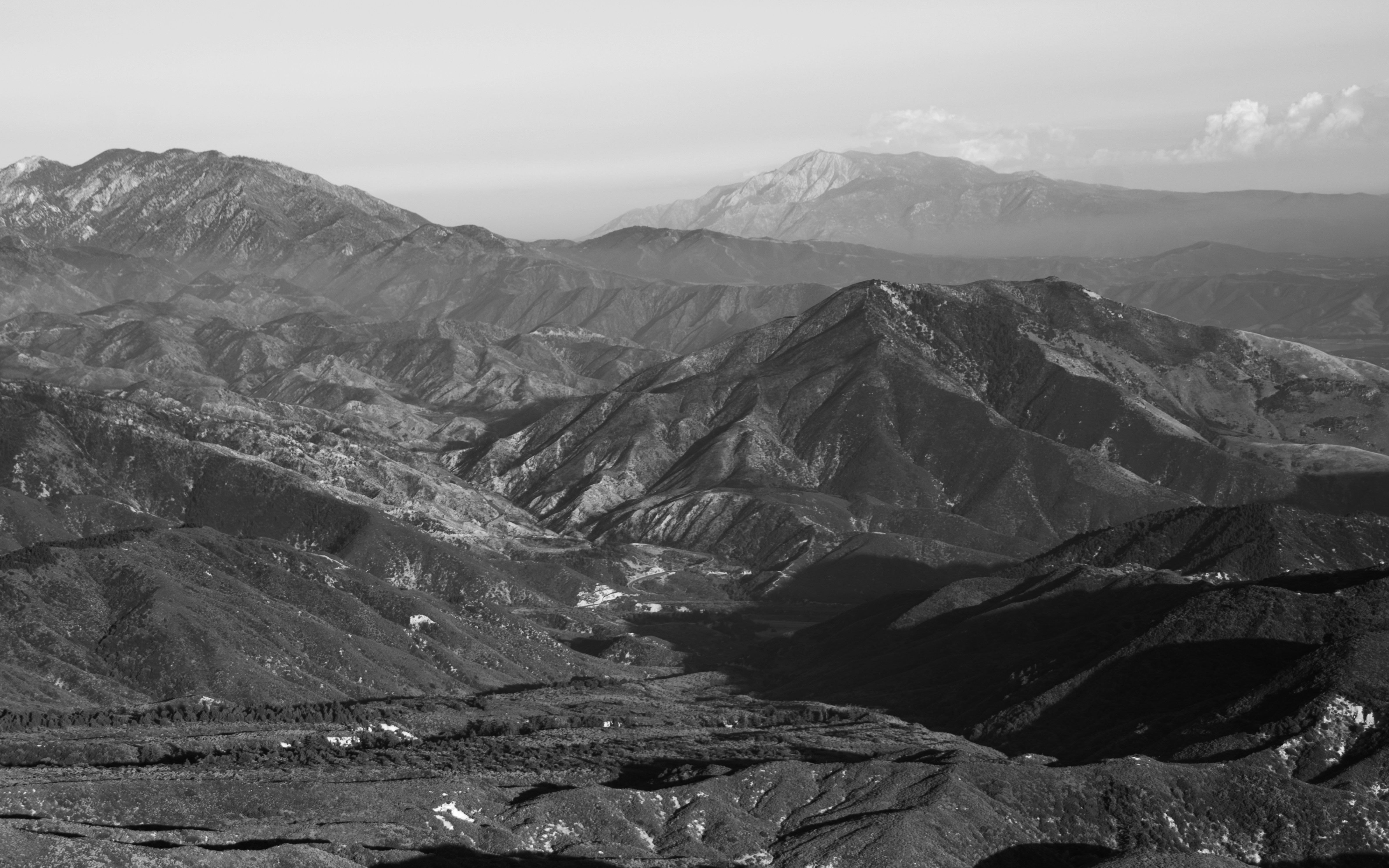 Dramatic black and white landscape showcasing a series of rugged mountain ridges and valleys under a vast sky.