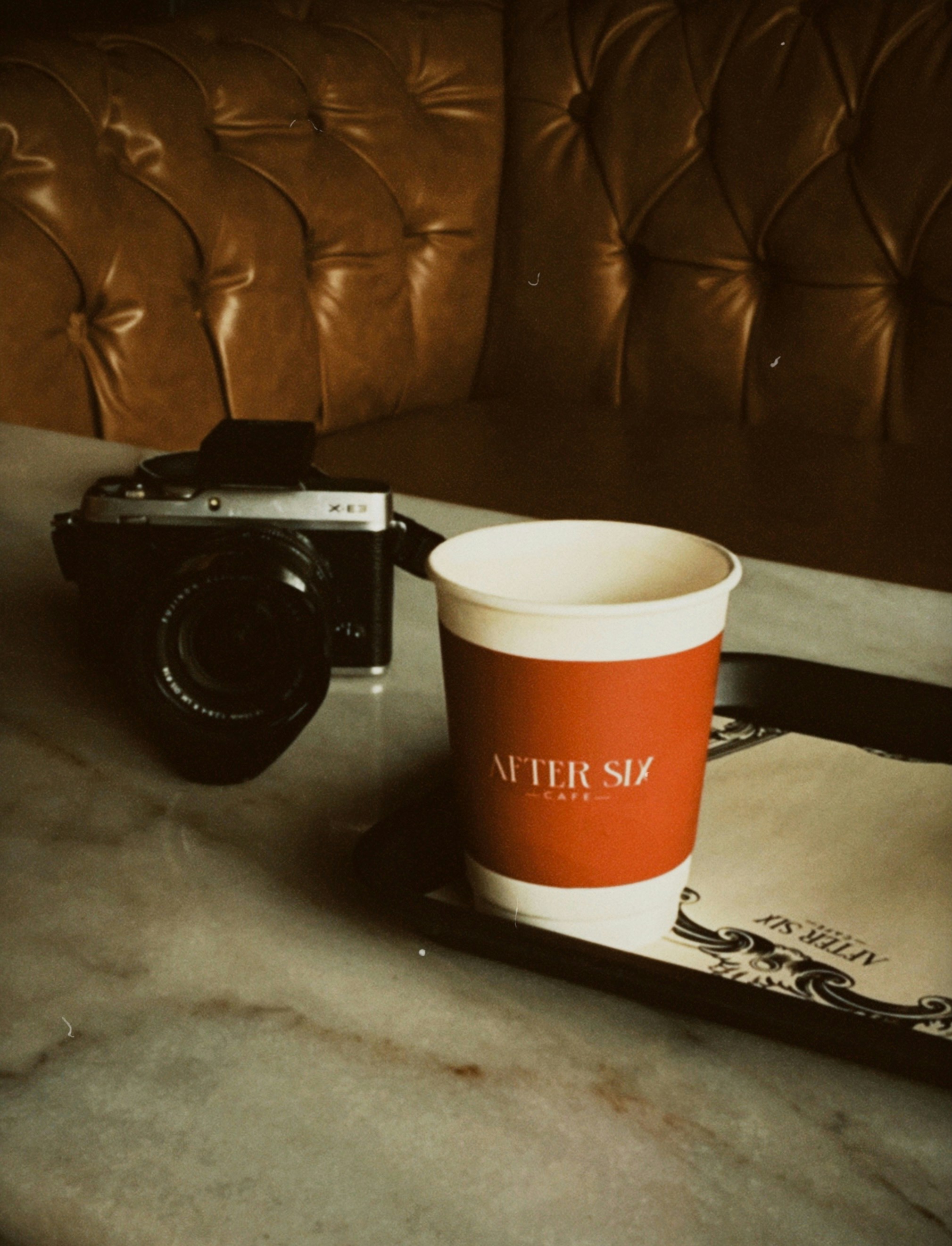 Coffee cup and vintage camera on a marble table in a cozy café setting.