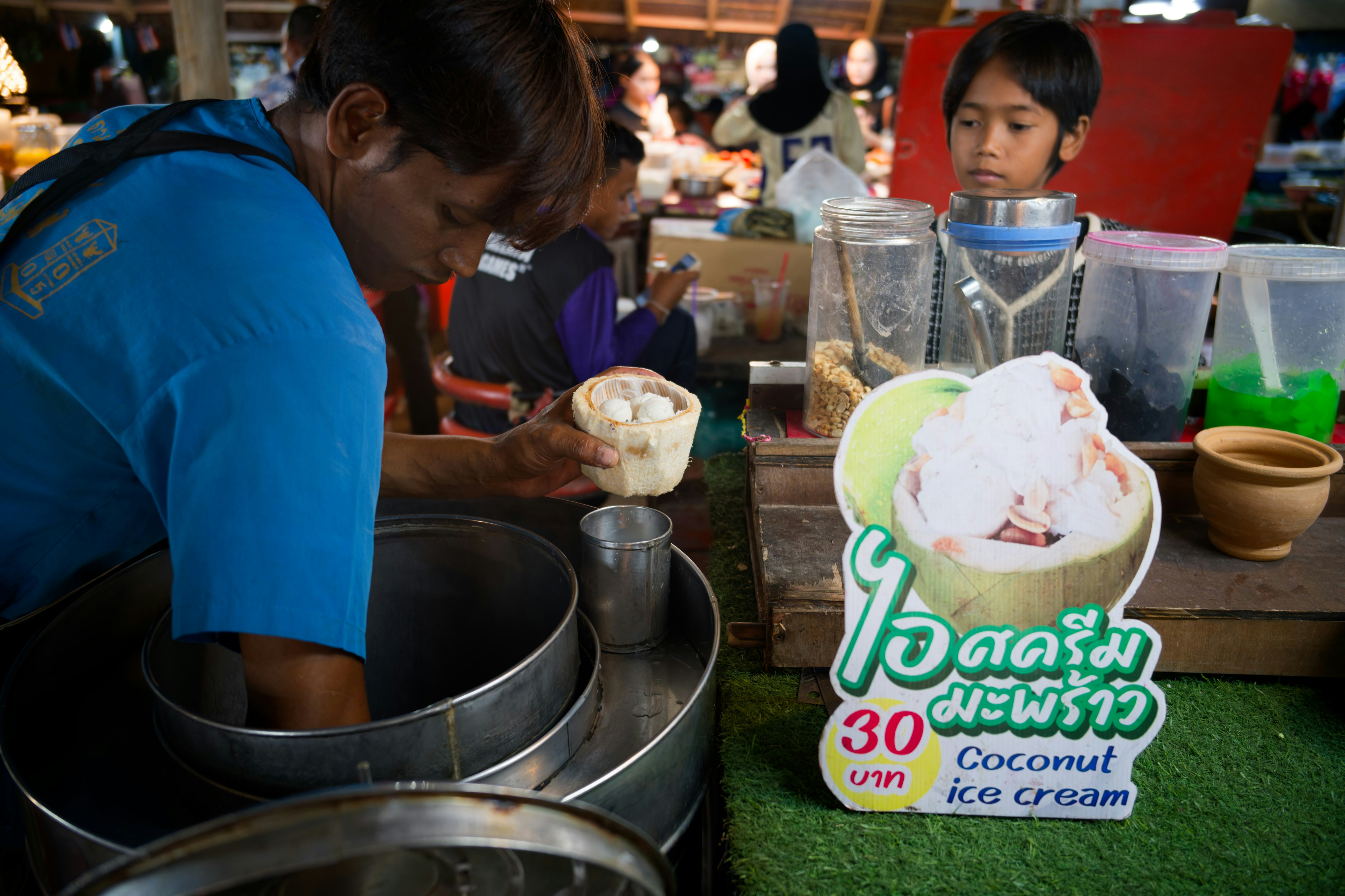 Vendor prepares coconut ice cream at market stall.