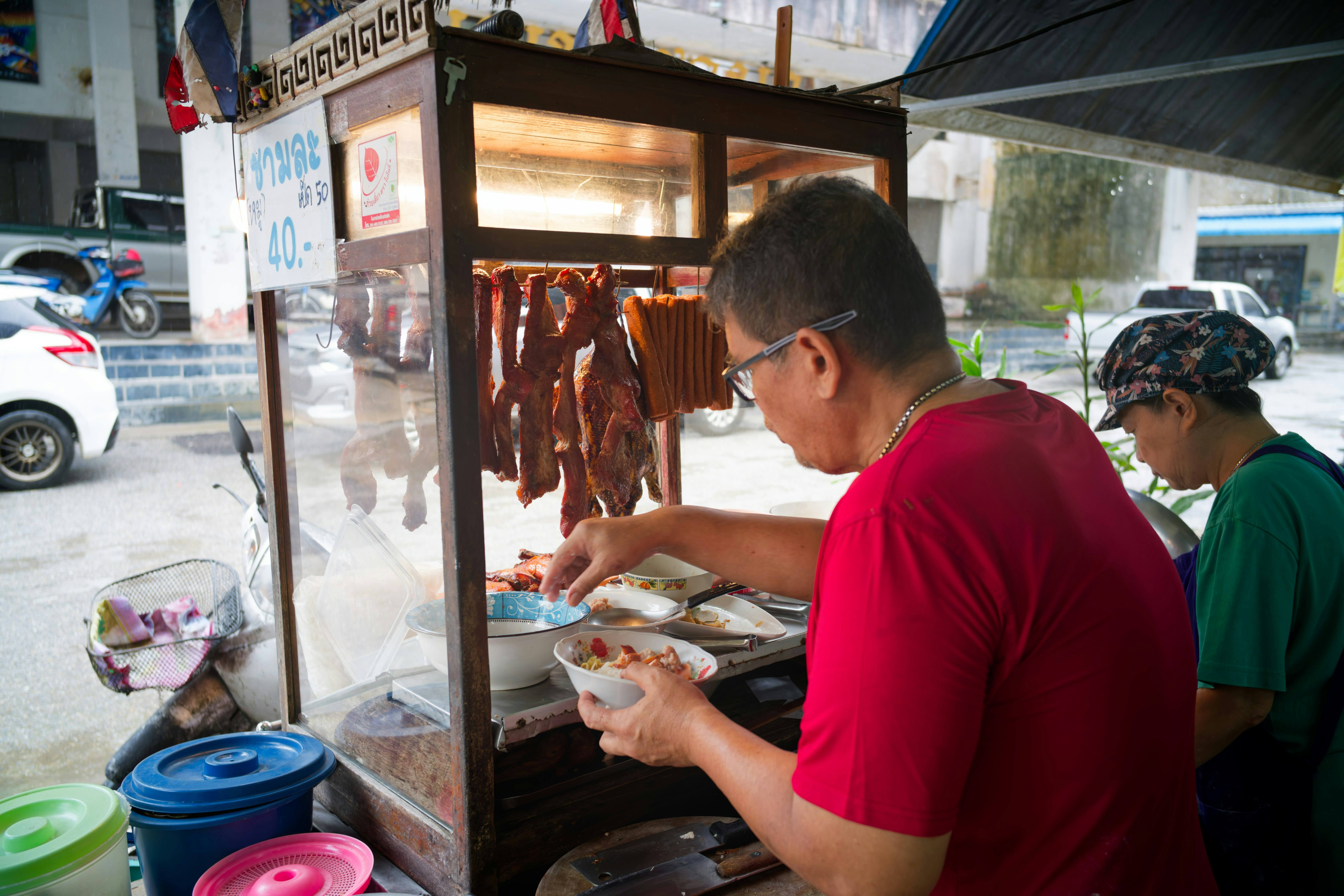 Glass-Front Sausage Stall Hustle: Red-Shirt Cook Serves Amid Hanging Meats