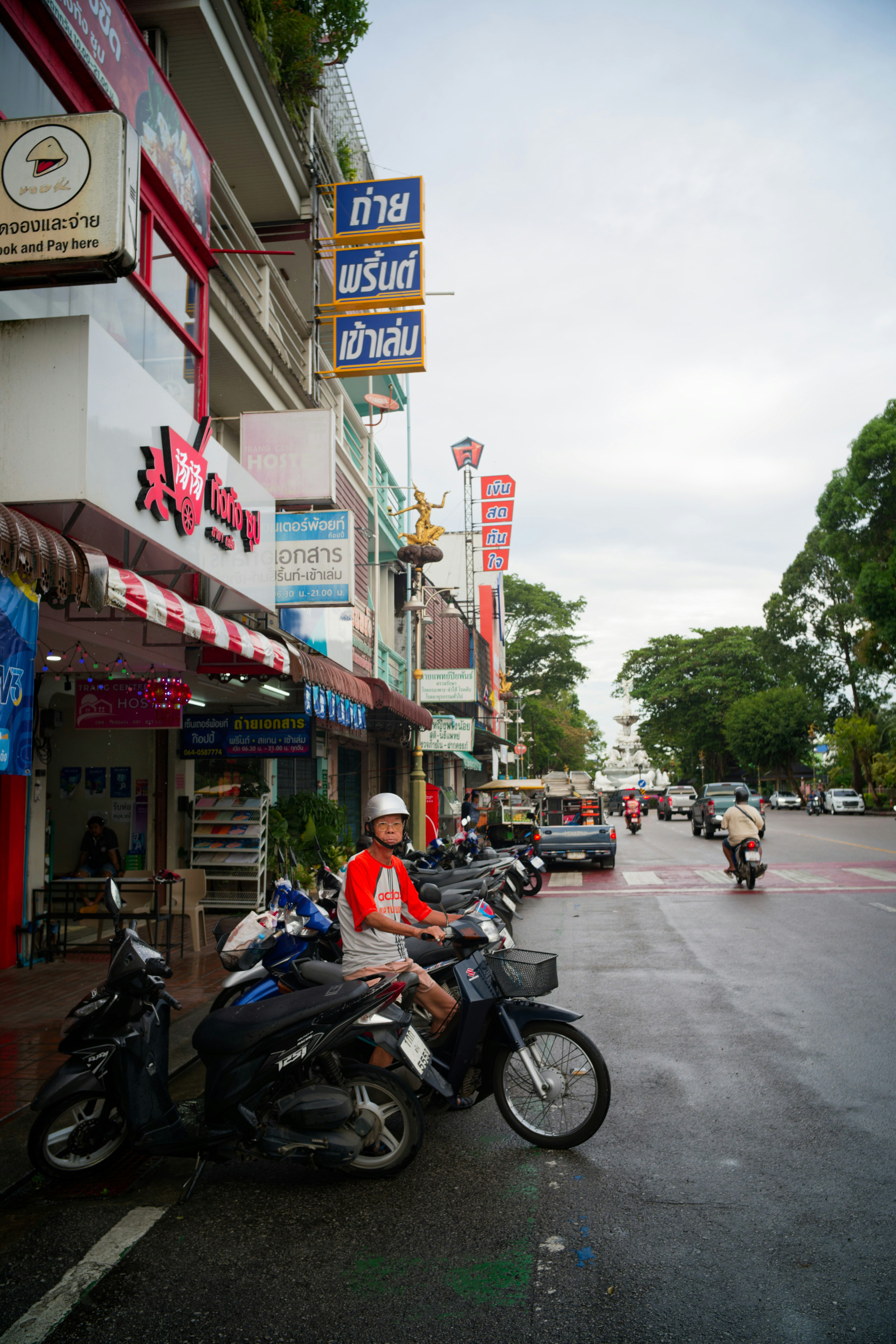 Man on scooter parked on wet street with shops