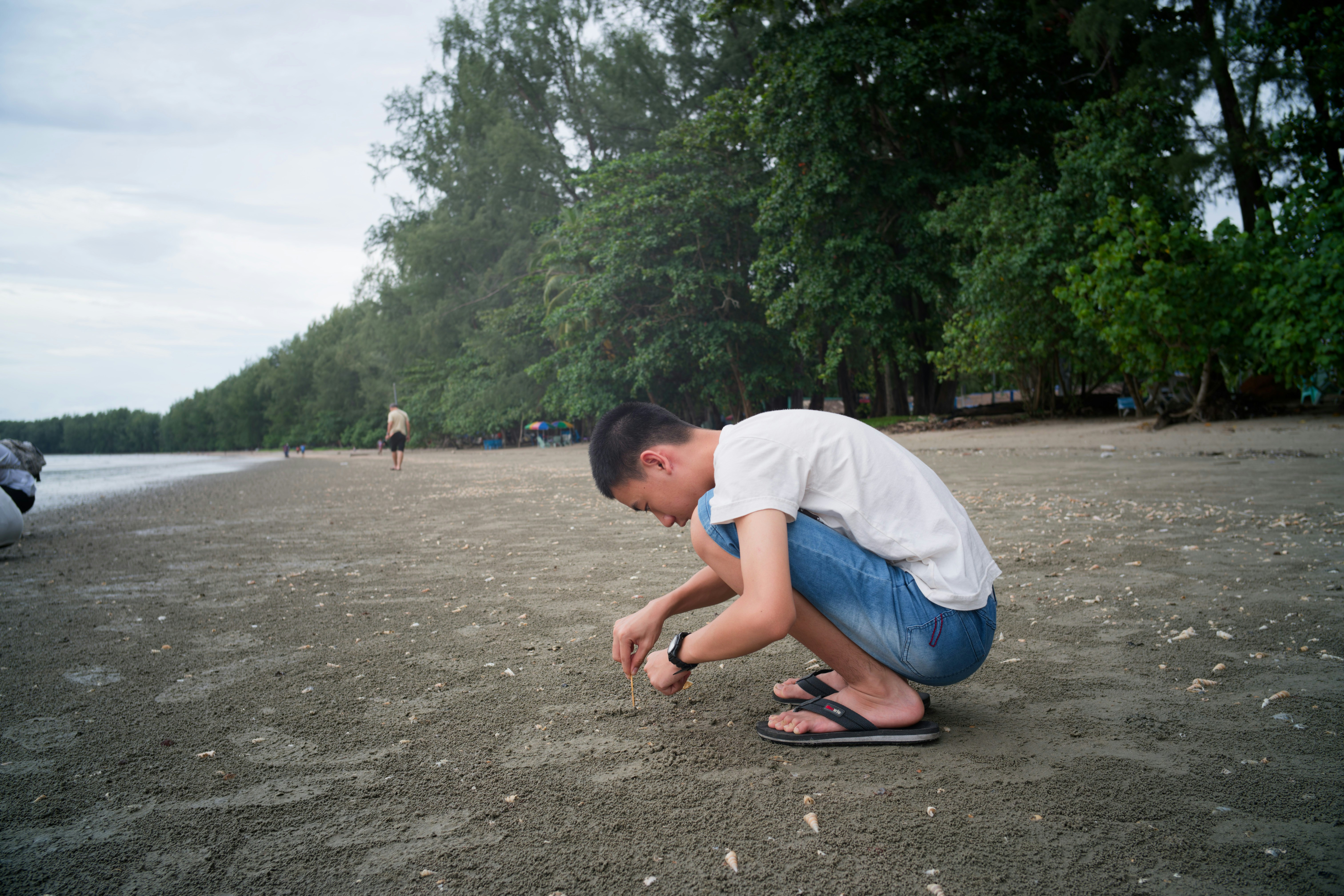 A person crouching on a sandy beach looking down.