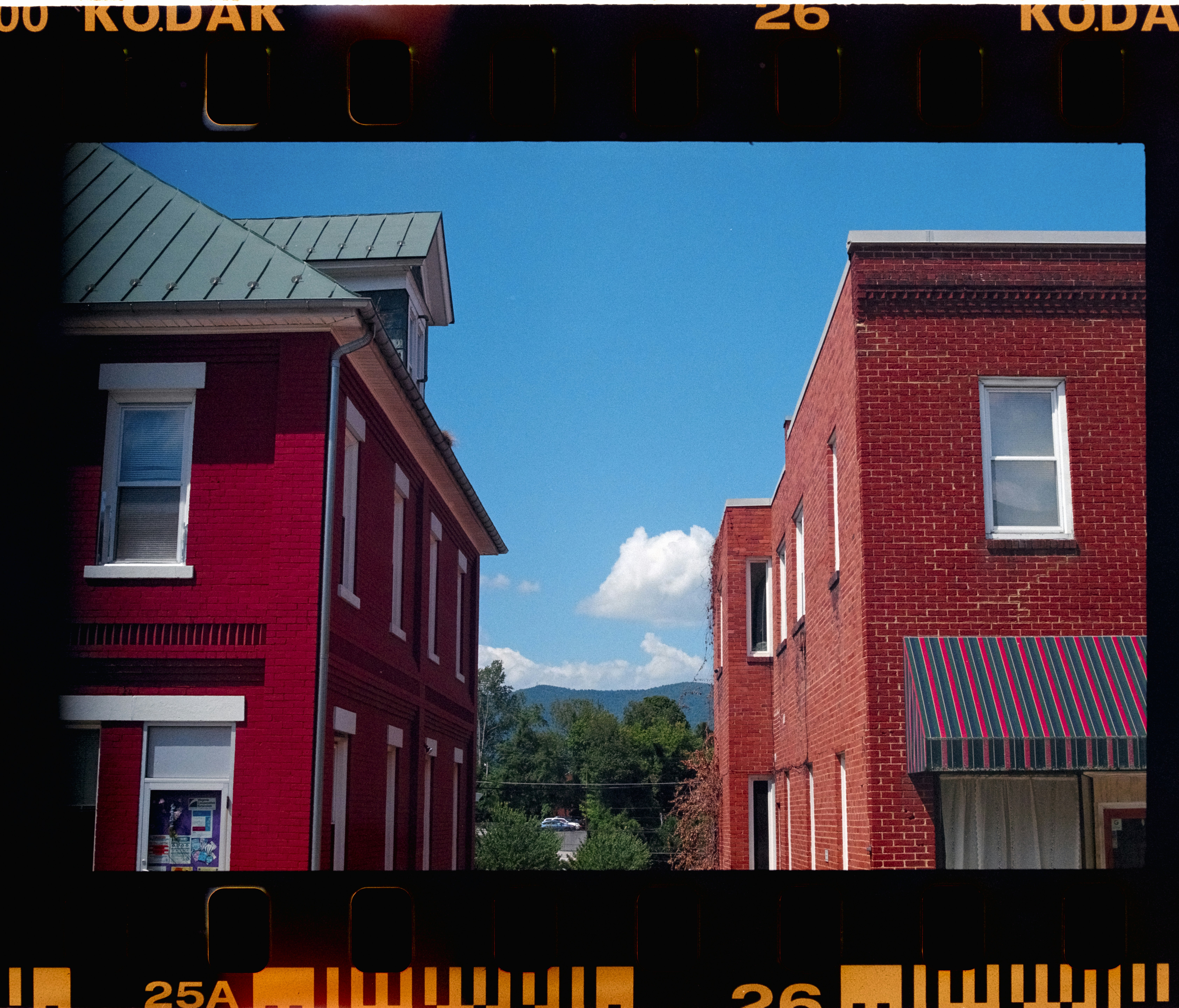 Two red brick buildings under a bright blue sky.