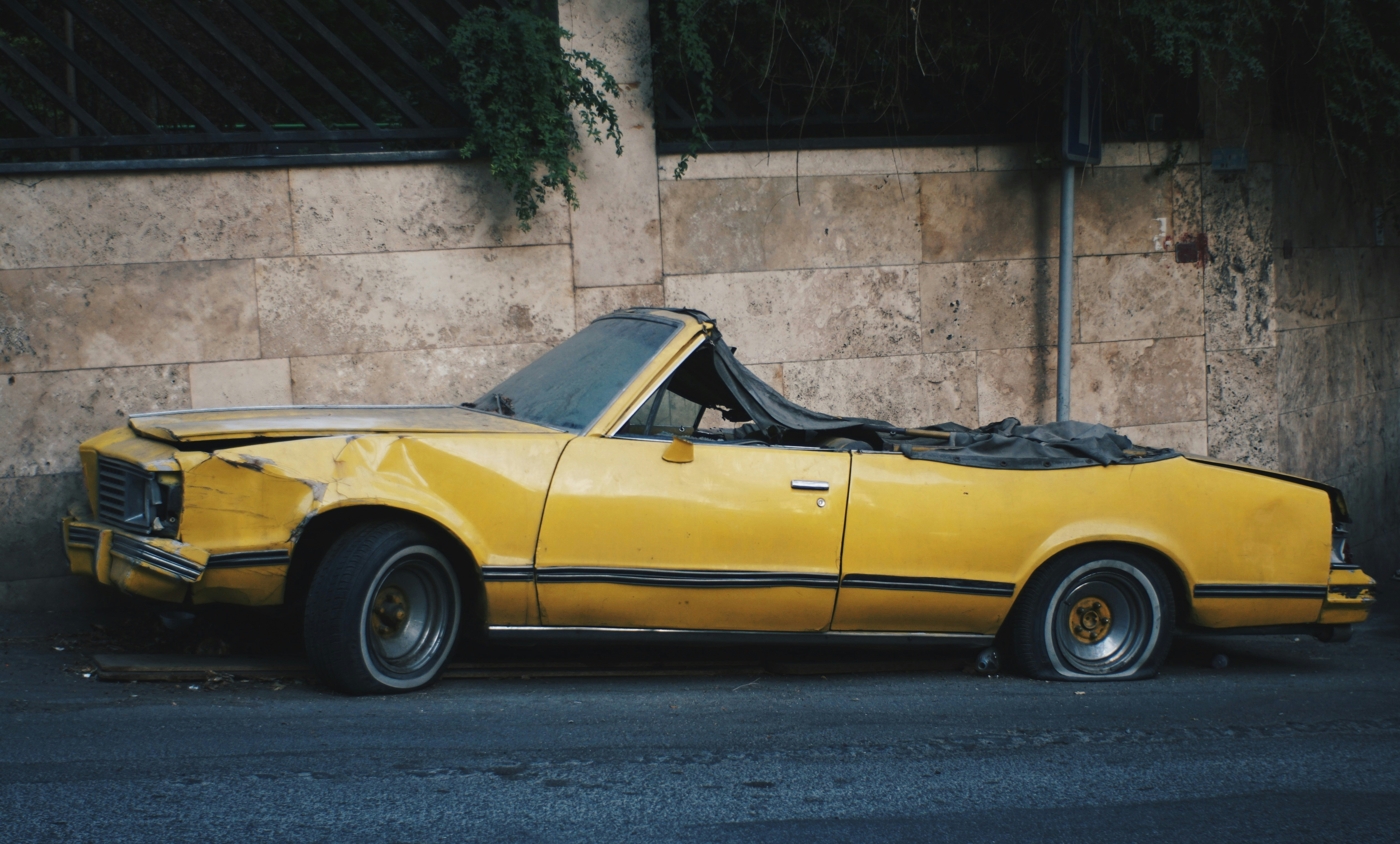 All out of road, all out of time. | A dilapidated yellow convertible car parked by a stone wall.