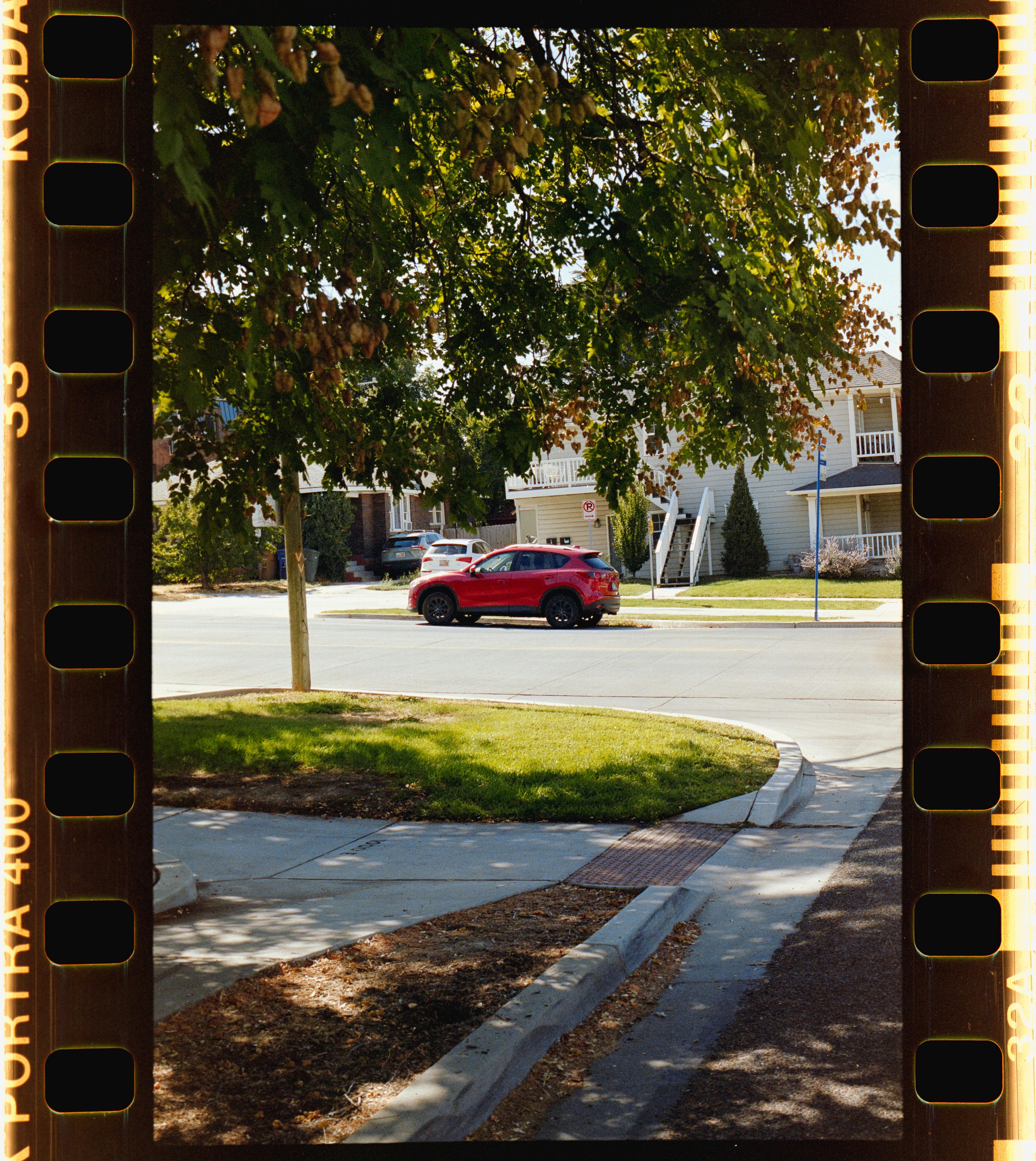 A red vehicle navigating a suburban intersection framed by lush greenery and residential homes. The scene captures the essence of urban living.