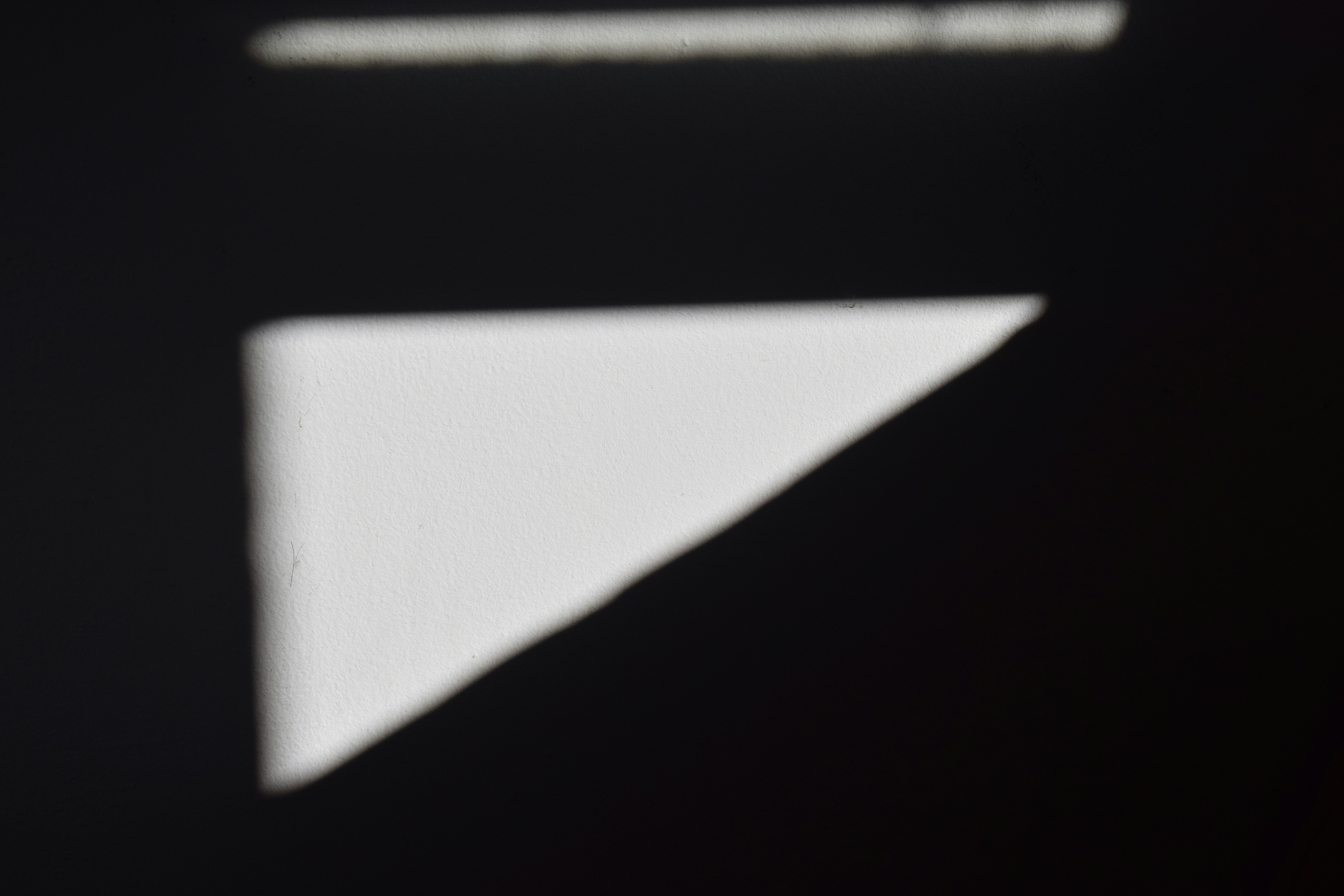 A white triangle casts a shadow on black.