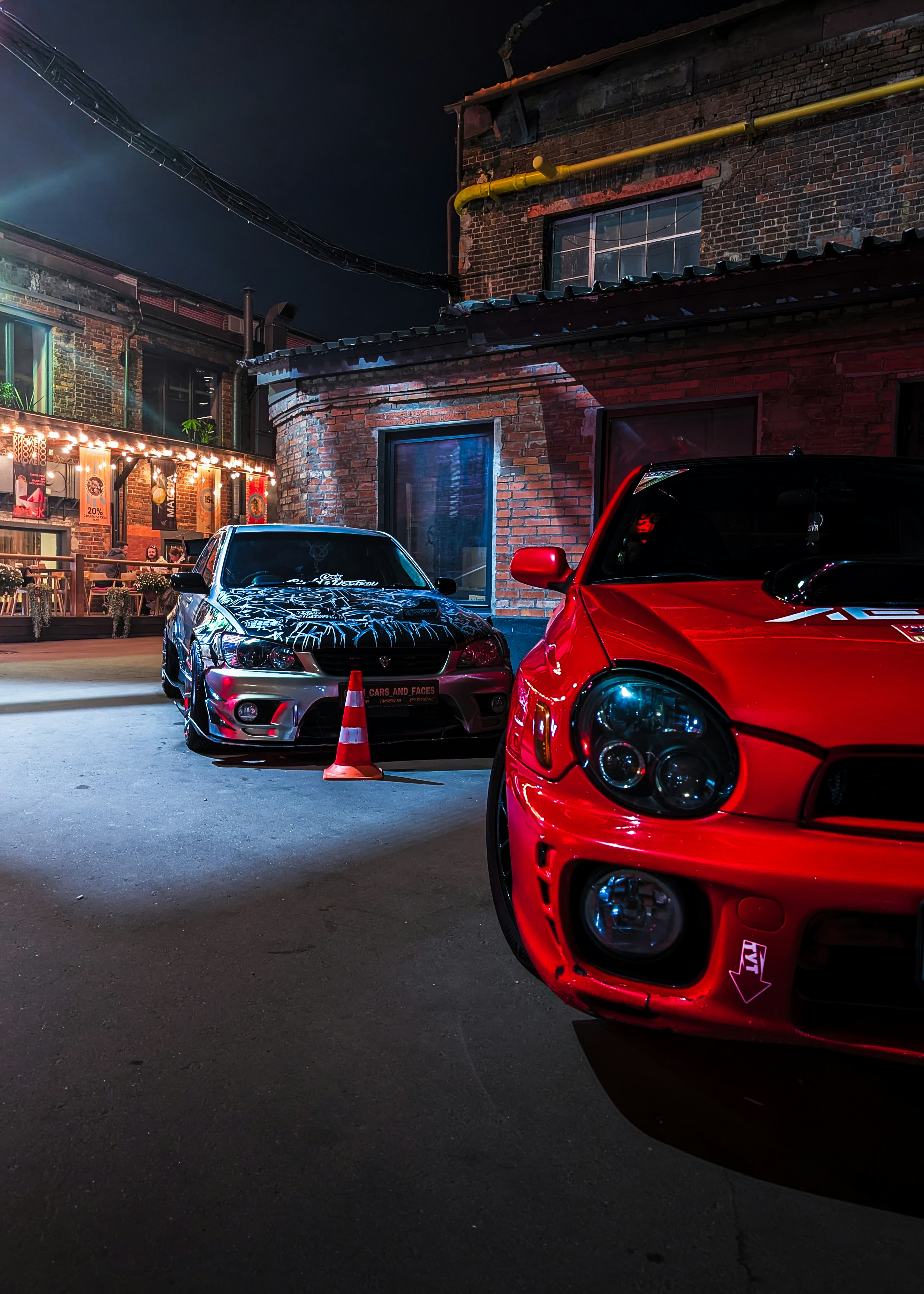 Two modified cars parked on a street at night.