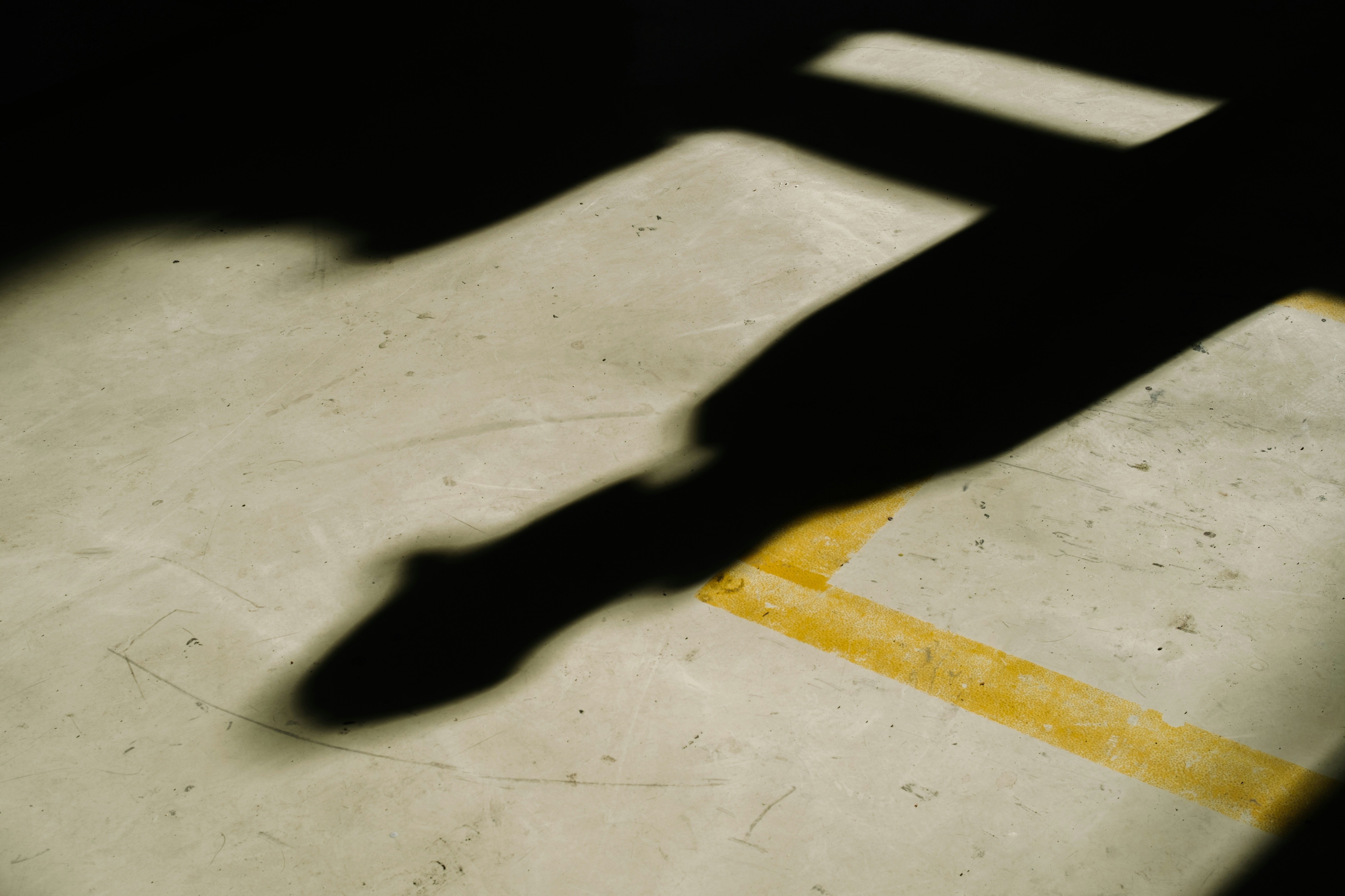 Abstract interplay of shadows cast on a concrete floor, highlighting a yellow line and creating a striking visual contrast.