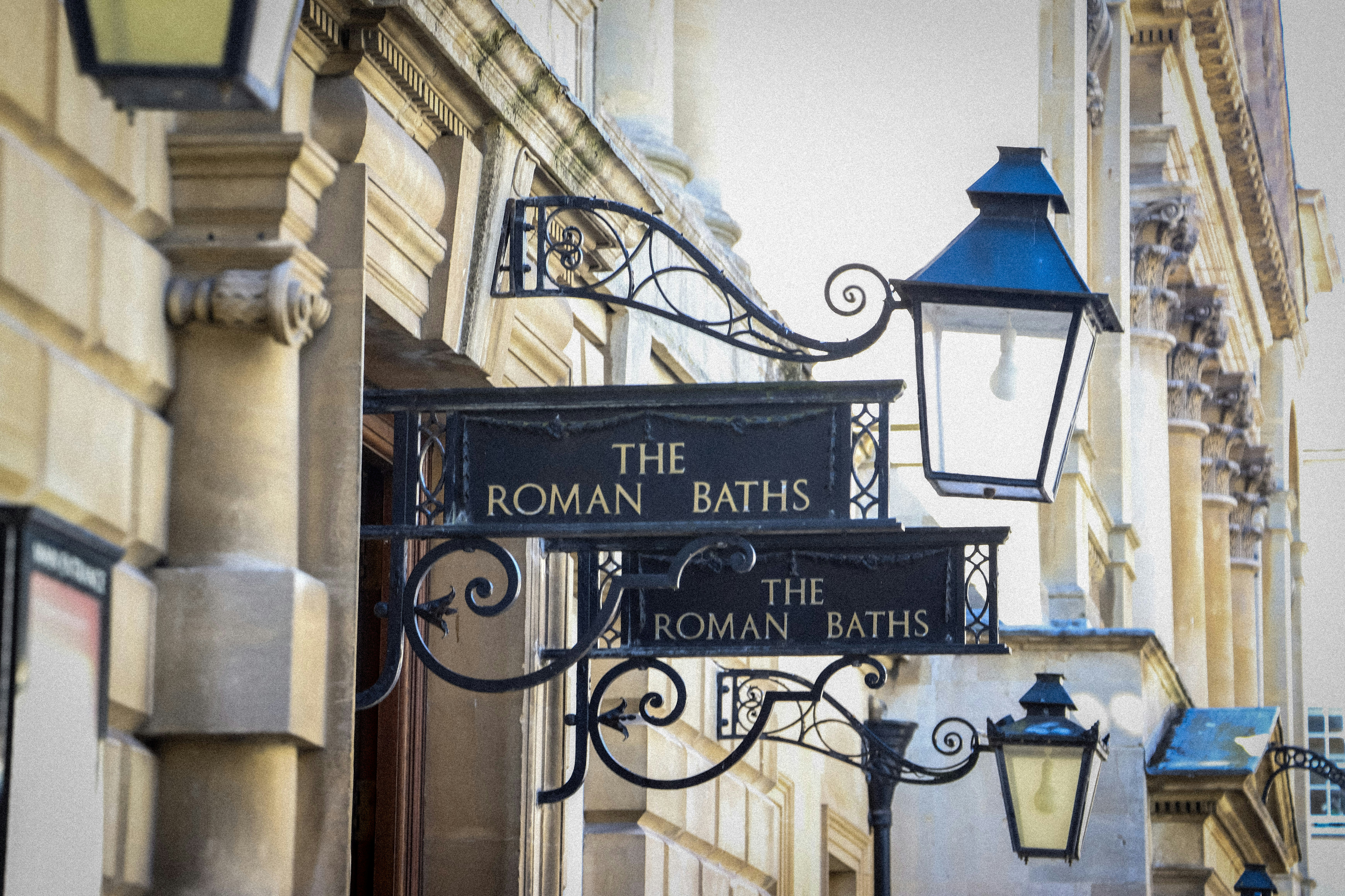Iron Sign Brackets Framing The Roman Baths: Lanterns and Limestone