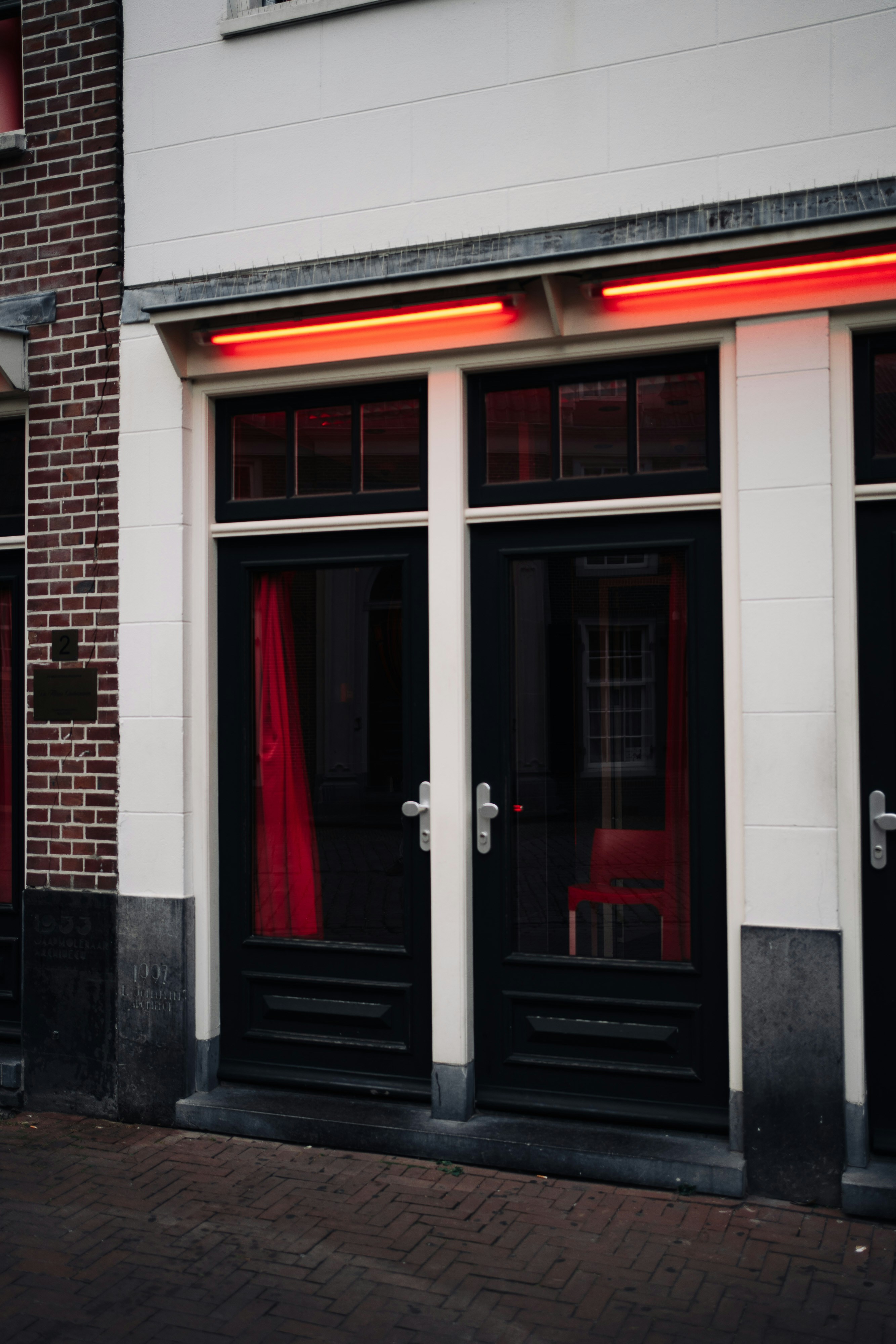 Two dark doors framed by red-lit accents, suggesting an intriguing atmosphere. The contrasting elements evoke a sense of mystery.
