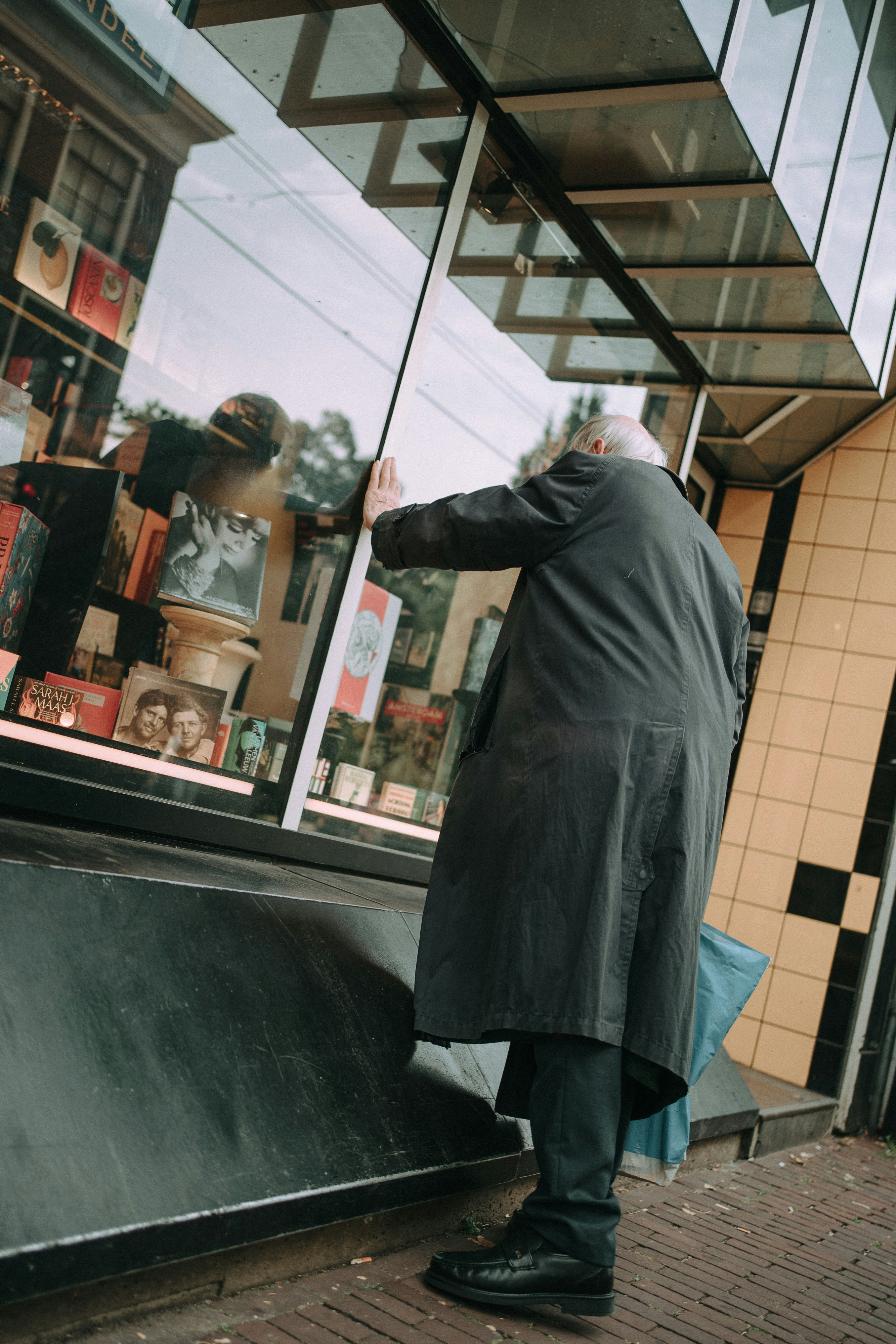 Elderly man peering into a shop window filled with vintage books and photographs, evoking nostalgia and curiosity.