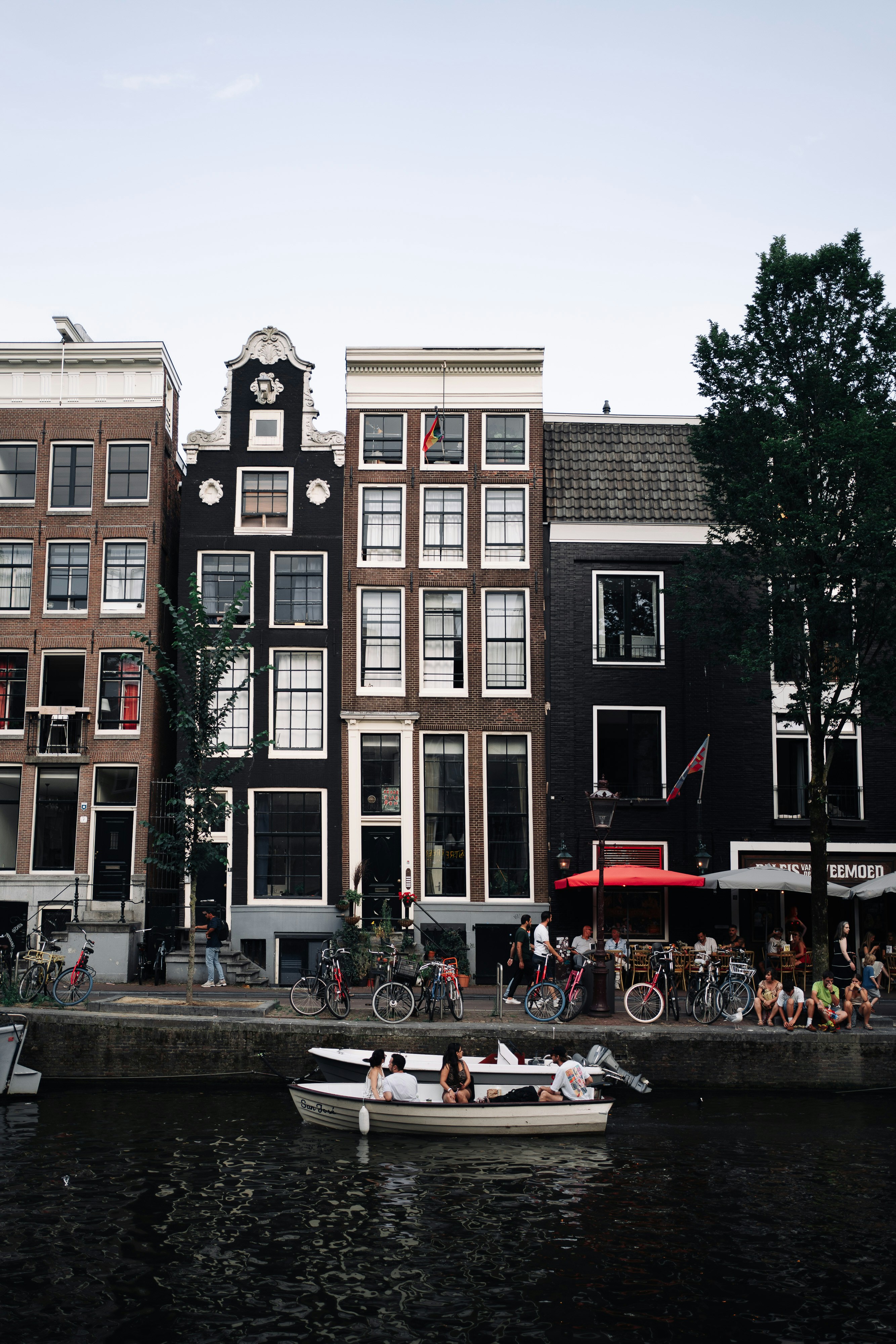 Quaint canal-side buildings reflect Amsterdam's architectural beauty, while a small boat carries relaxed passengers along the waterway.