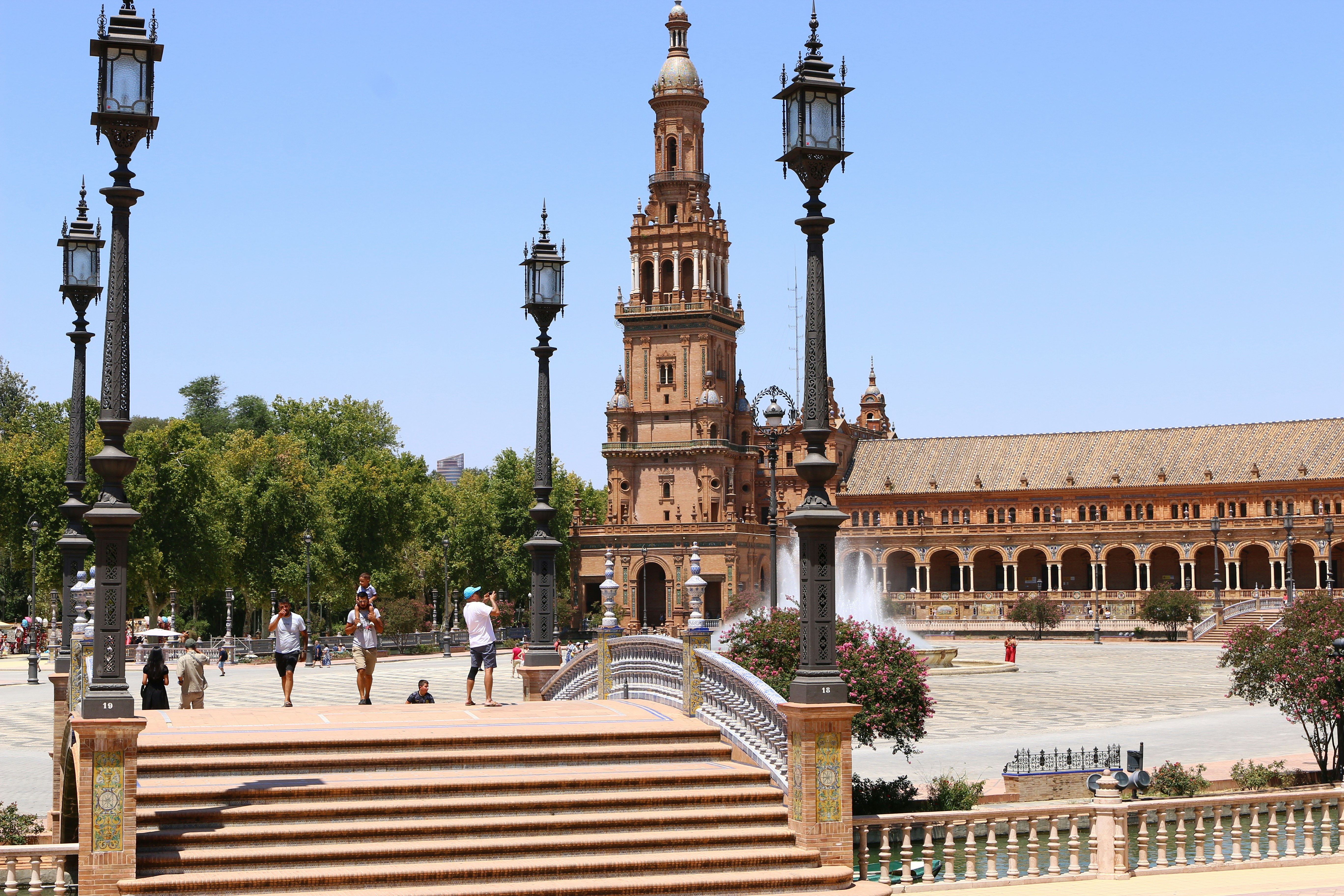 Plaza de España, Seville Andalusia | Ornate bridge leading to a grand building with a tower.