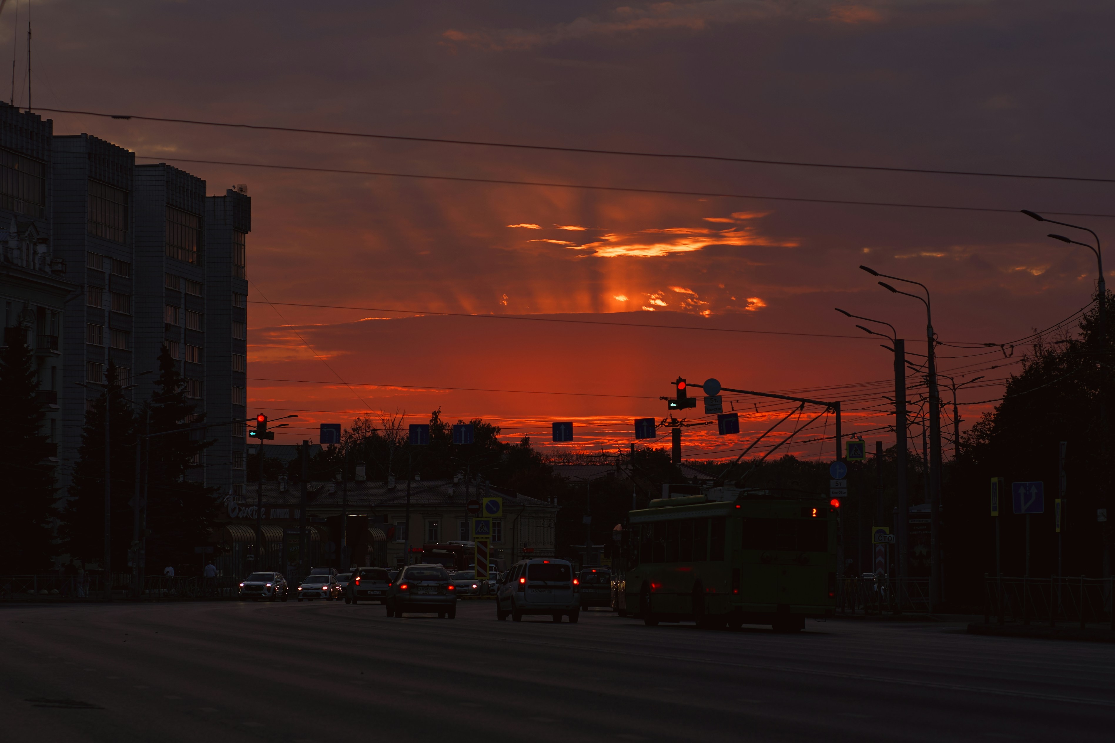 Vibrant sunset casting rays over a bustling city intersection, with silhouettes of vehicles and buildings. 