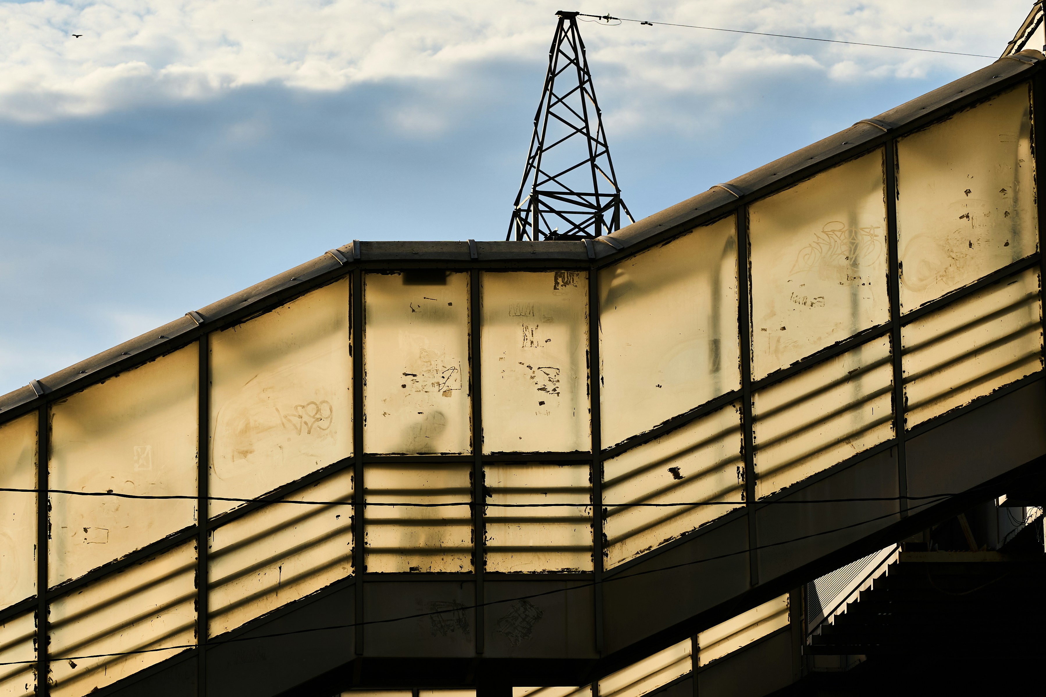 Translucent overpass structure illuminated by the sun, showcasing intricate lines and textures against a cloudy sky.