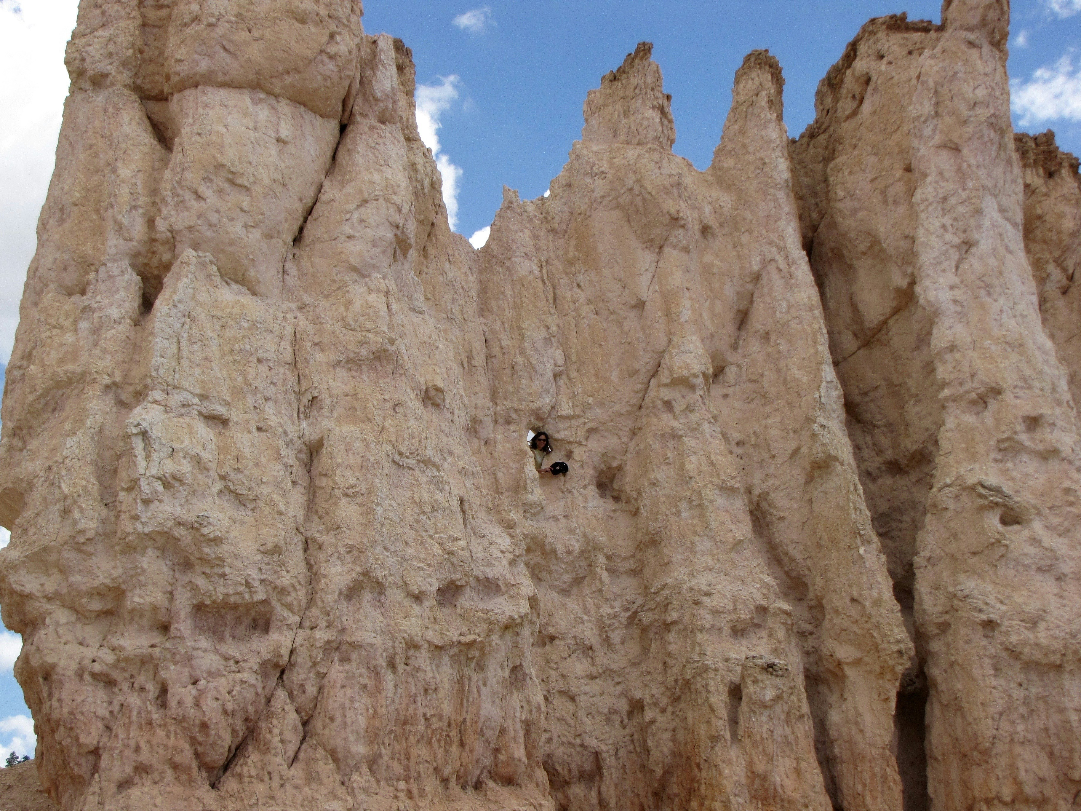 Vertical rock formations rise dramatically against a blue sky, showcasing the rugged beauty of natural erosion. A climber is visible, adding a sense of scale to the landscape.