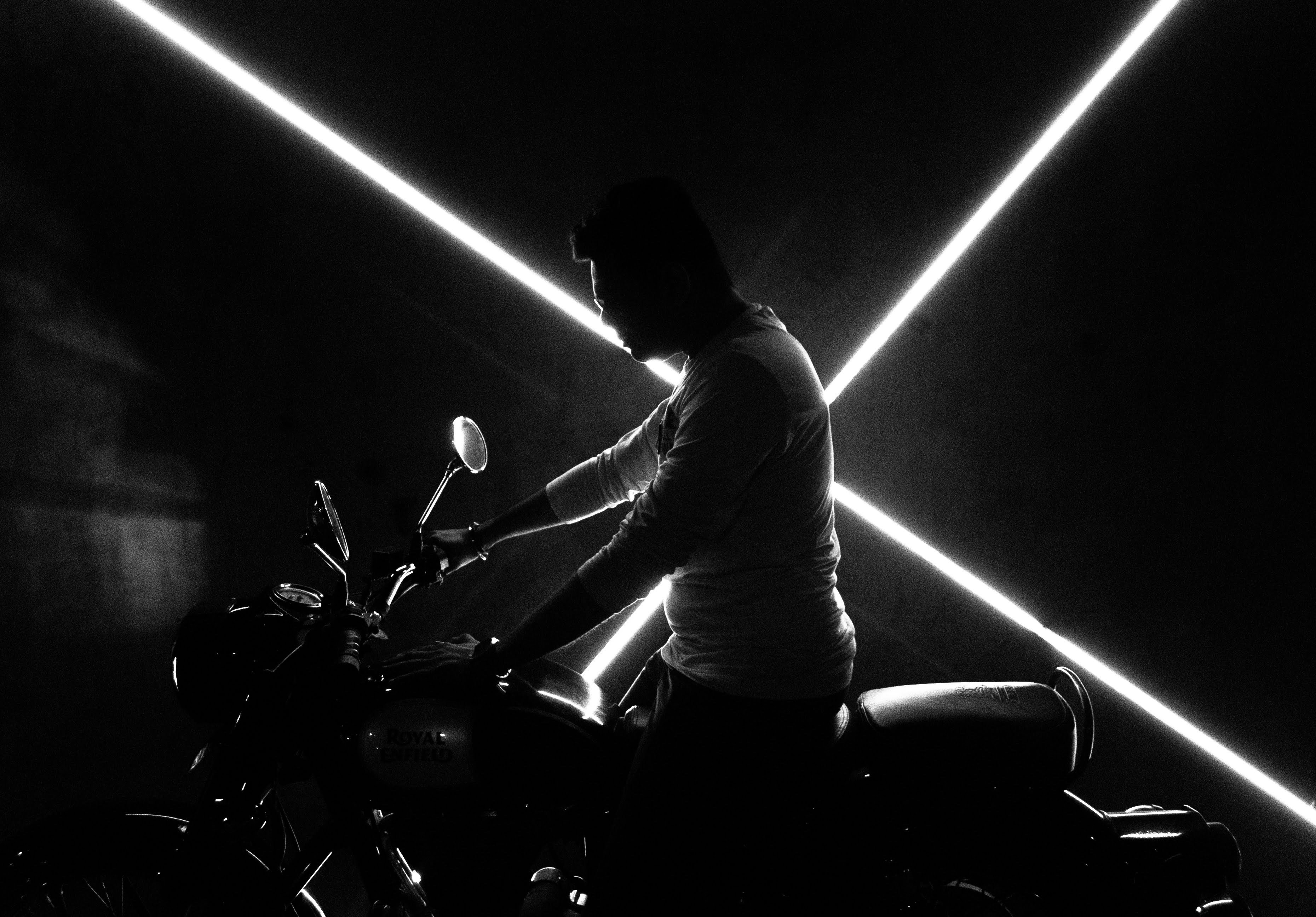 Silhouette of a rider poised on a motorcycle, framed by intersecting beams of light against a dark backdrop.