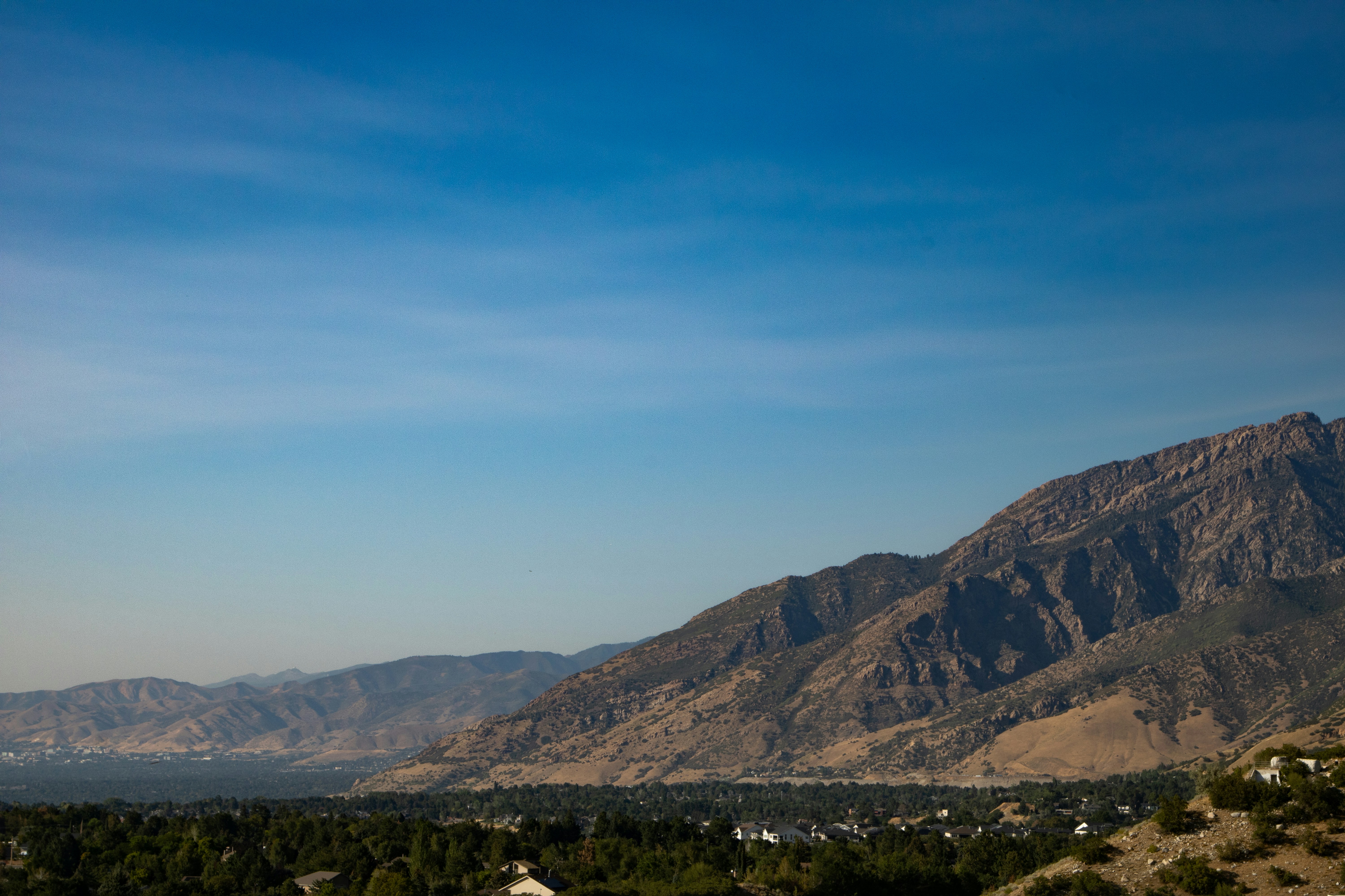 A panoramic view of a mountainous landscape under a clear blue sky, showcasing the rugged terrain and lush valleys below.