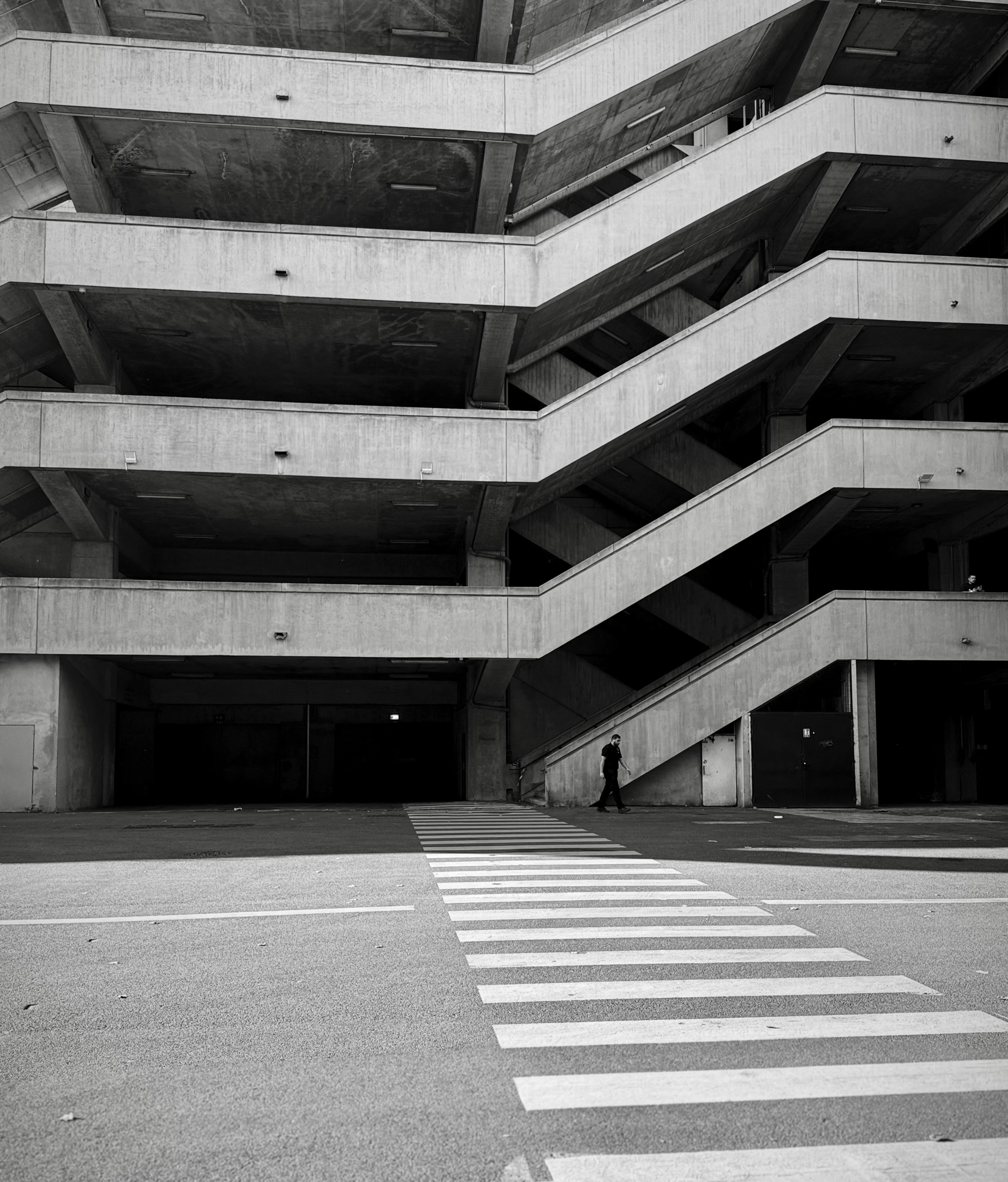 A lone figure walks up stairs in brutalist concrete structure.
