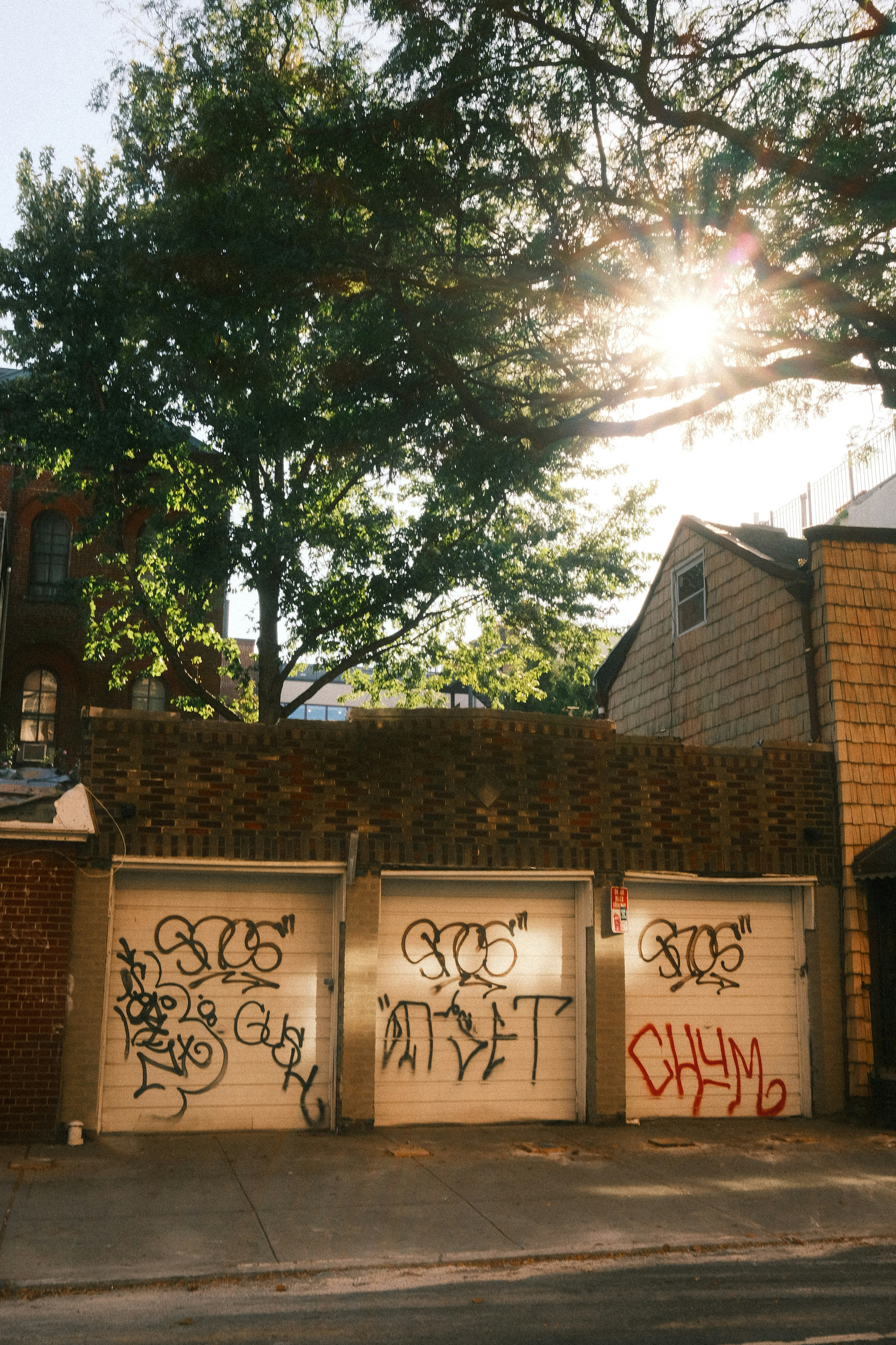 Three garage doors covered in graffiti under trees.