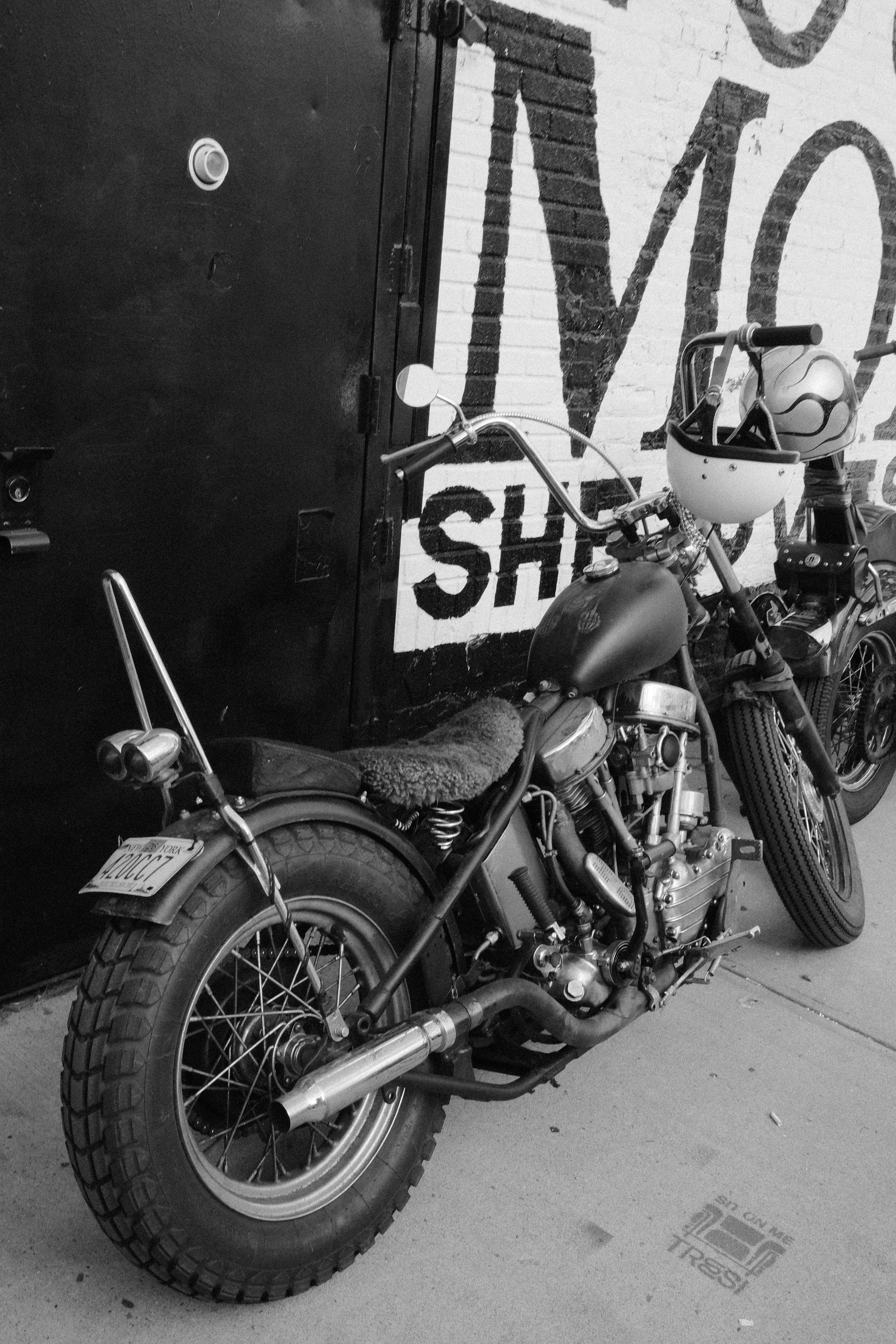 Two custom motorcycles parked outside a brick wall.
