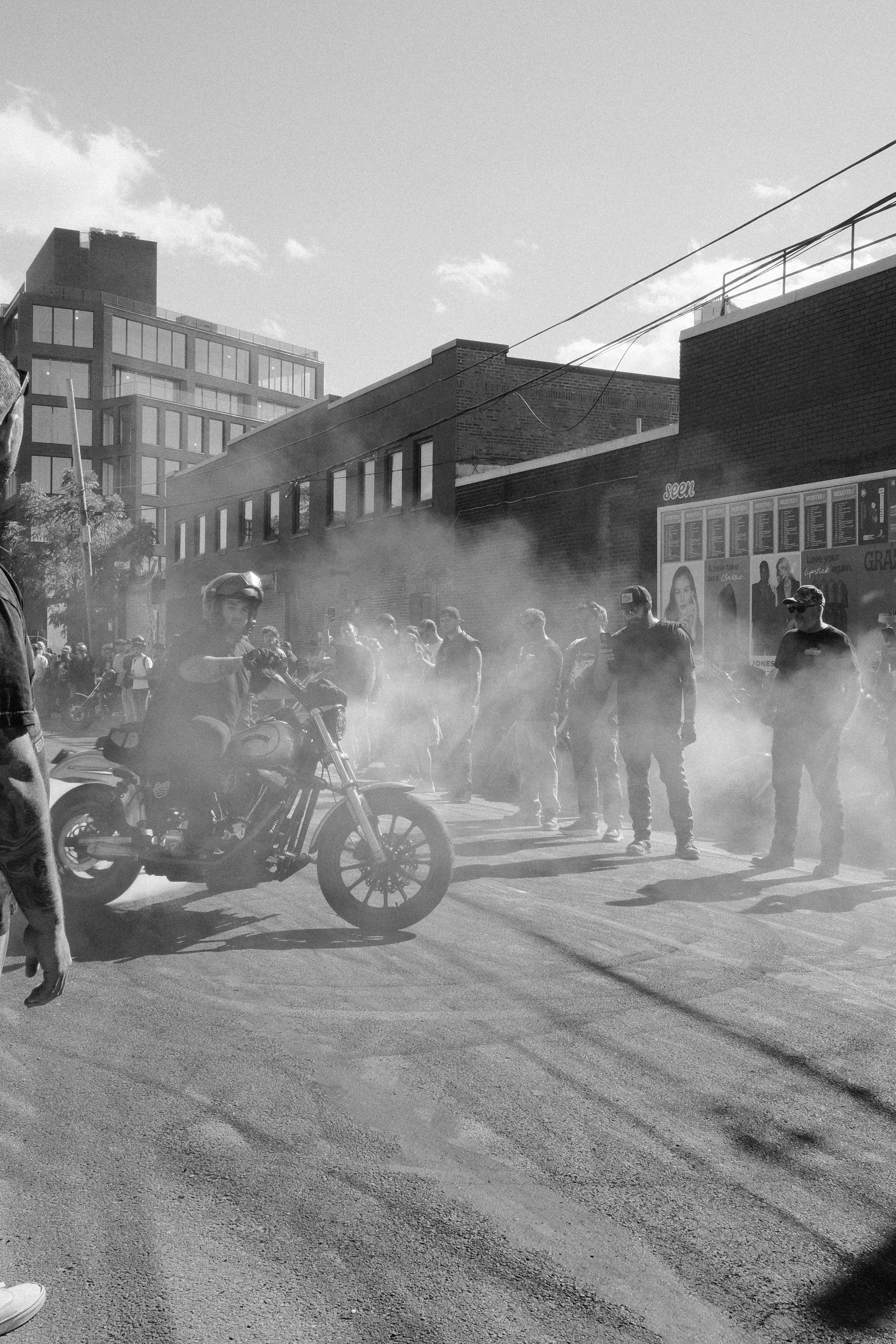 Motorcyclist maneuvering through a smoky street surrounded by onlookers in an urban setting.