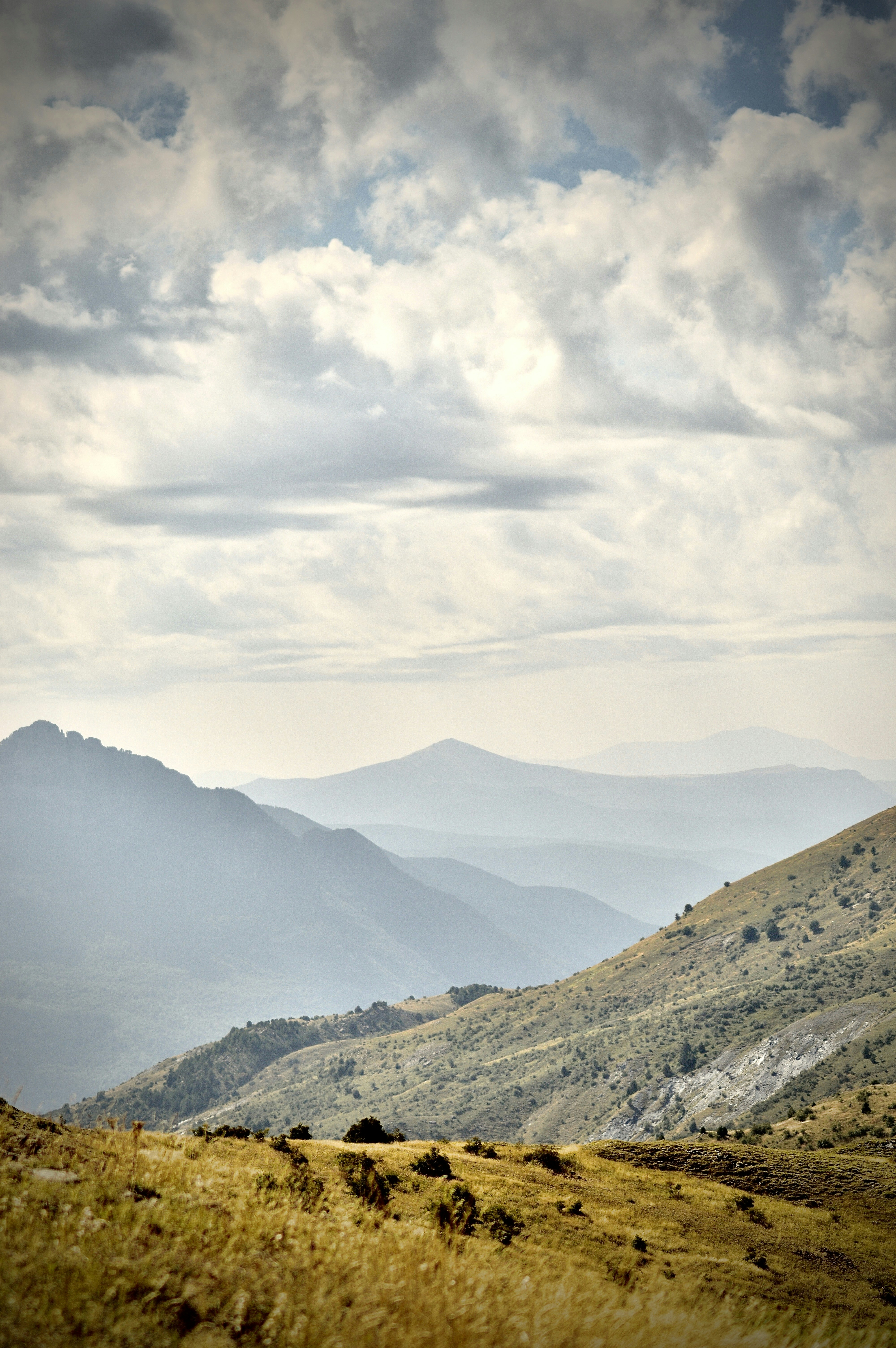 Expansive view of layered mountains under a cloudy sky, showcasing the interplay of light and shadow across the landscape.