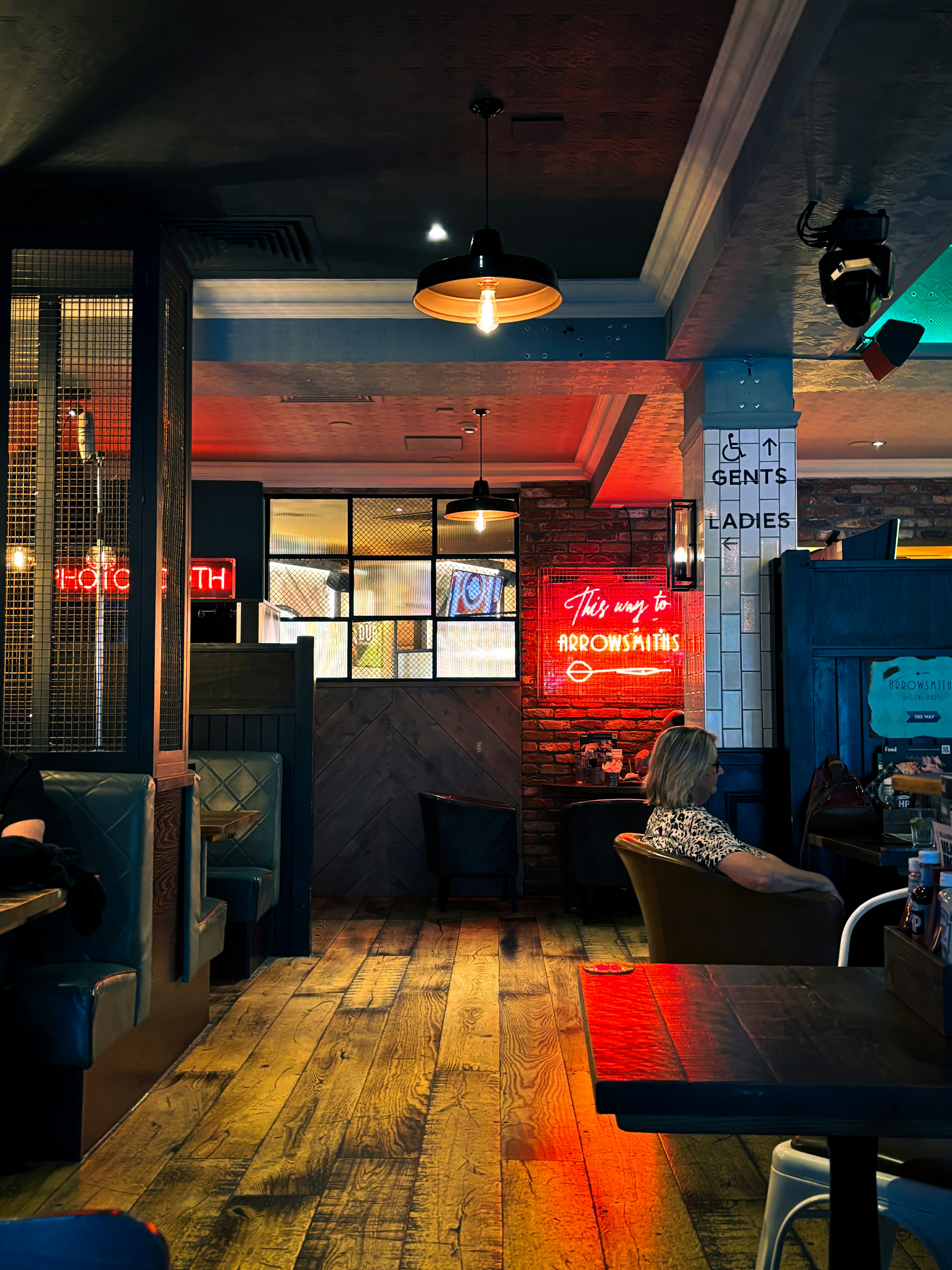 Neon sign directing patrons to the restrooms in a warmly lit pub interior, with wooden flooring and cozy seating areas.