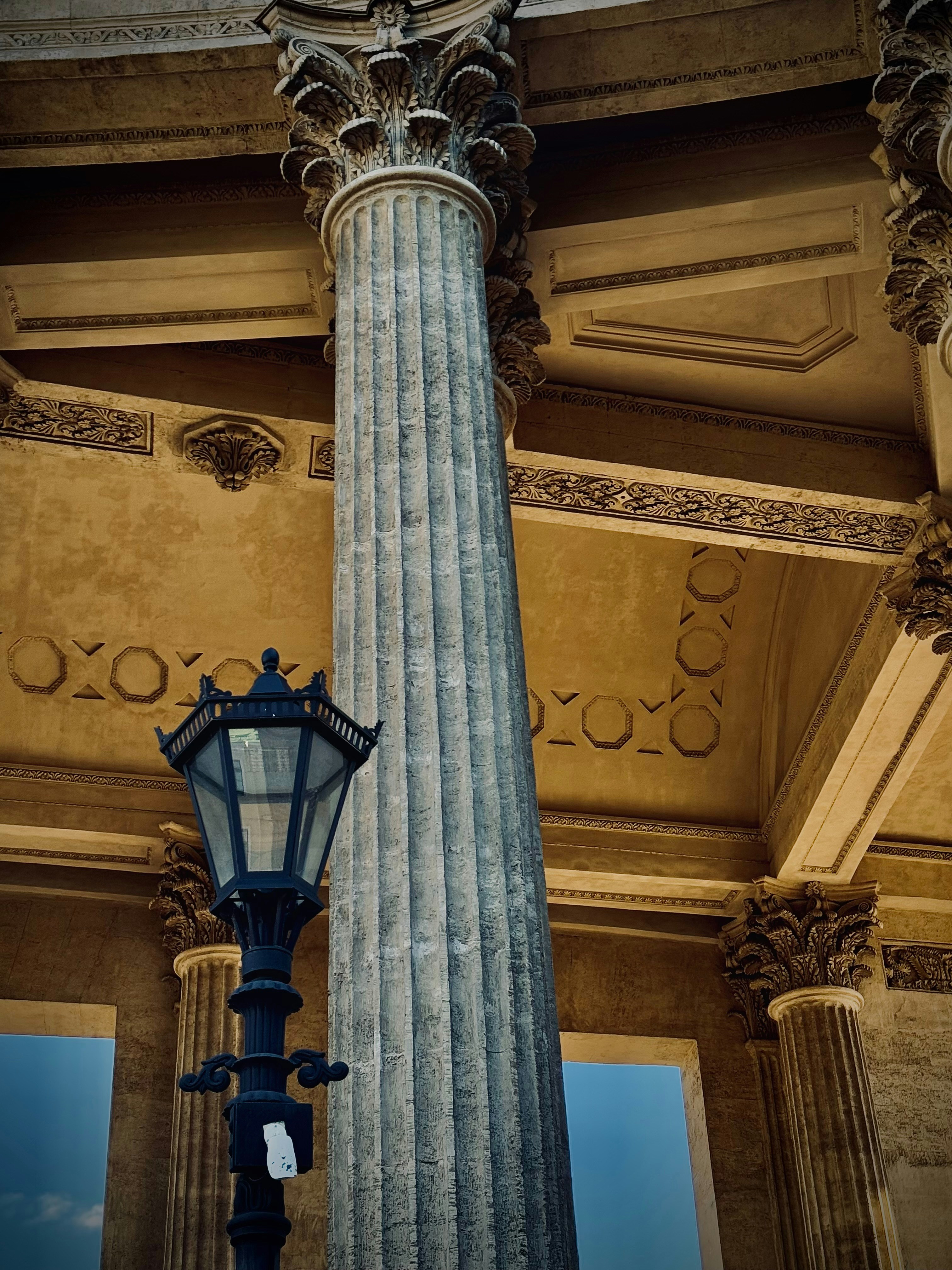 Intricate columns and a vintage lamppost beneath an ornate ceiling showcase classical architecture's elegance.