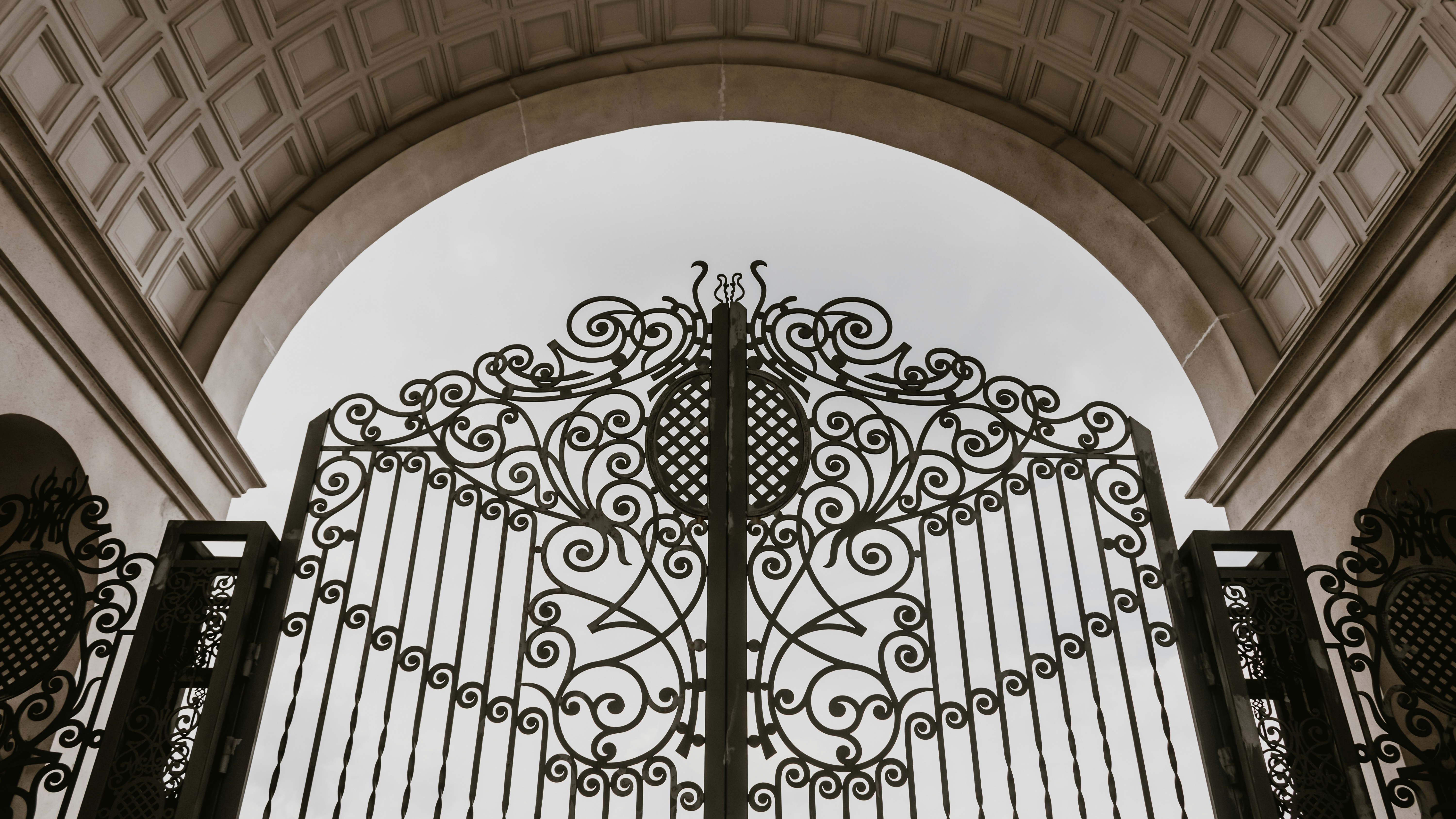 Intricately designed wrought iron gates under a grand archway, showcasing architectural elegance and detail.