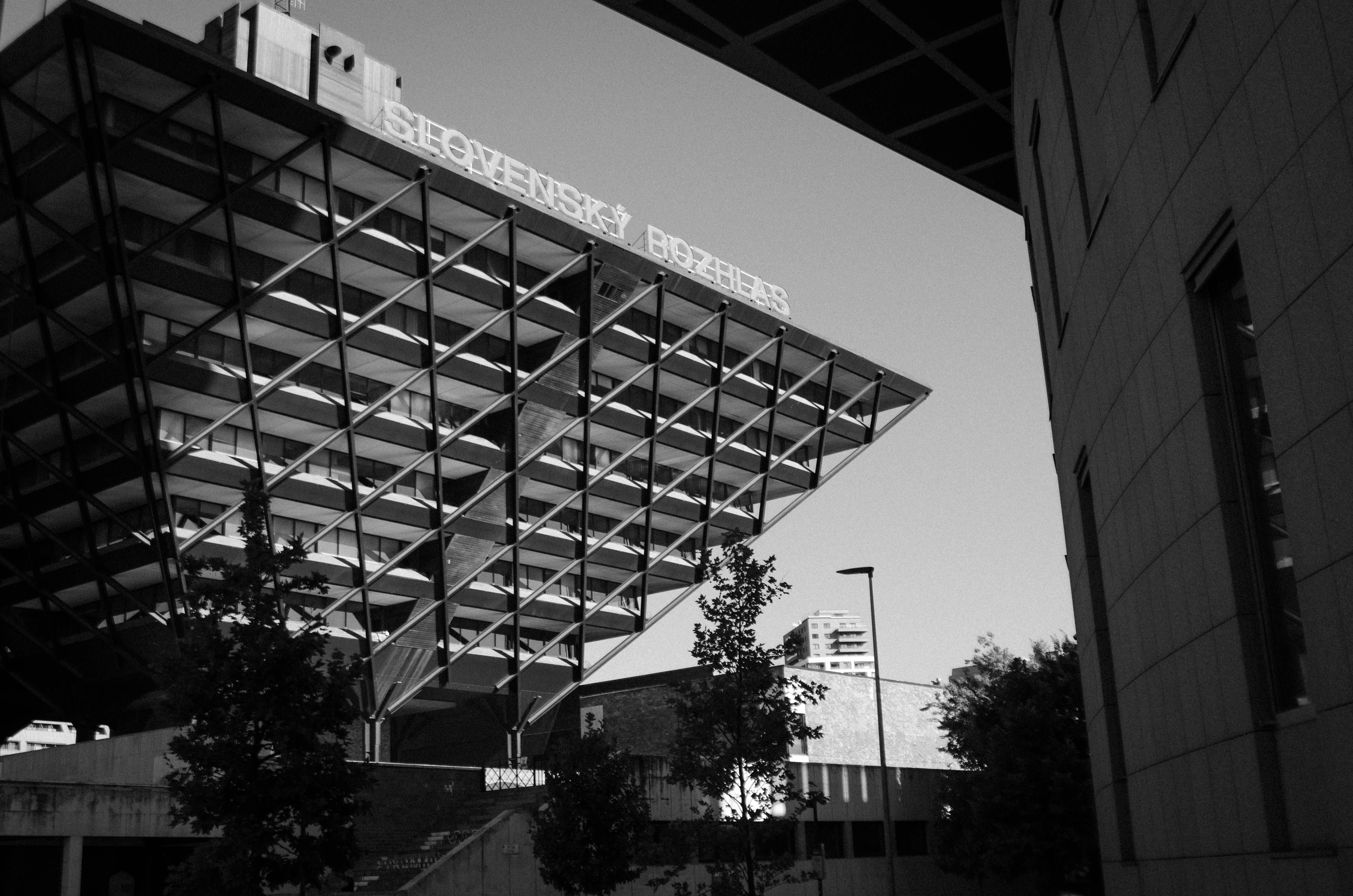 A striking modern building with a unique angular design, framed by surrounding greenery and urban elements. The monochrome aesthetic enhances the architectural details.