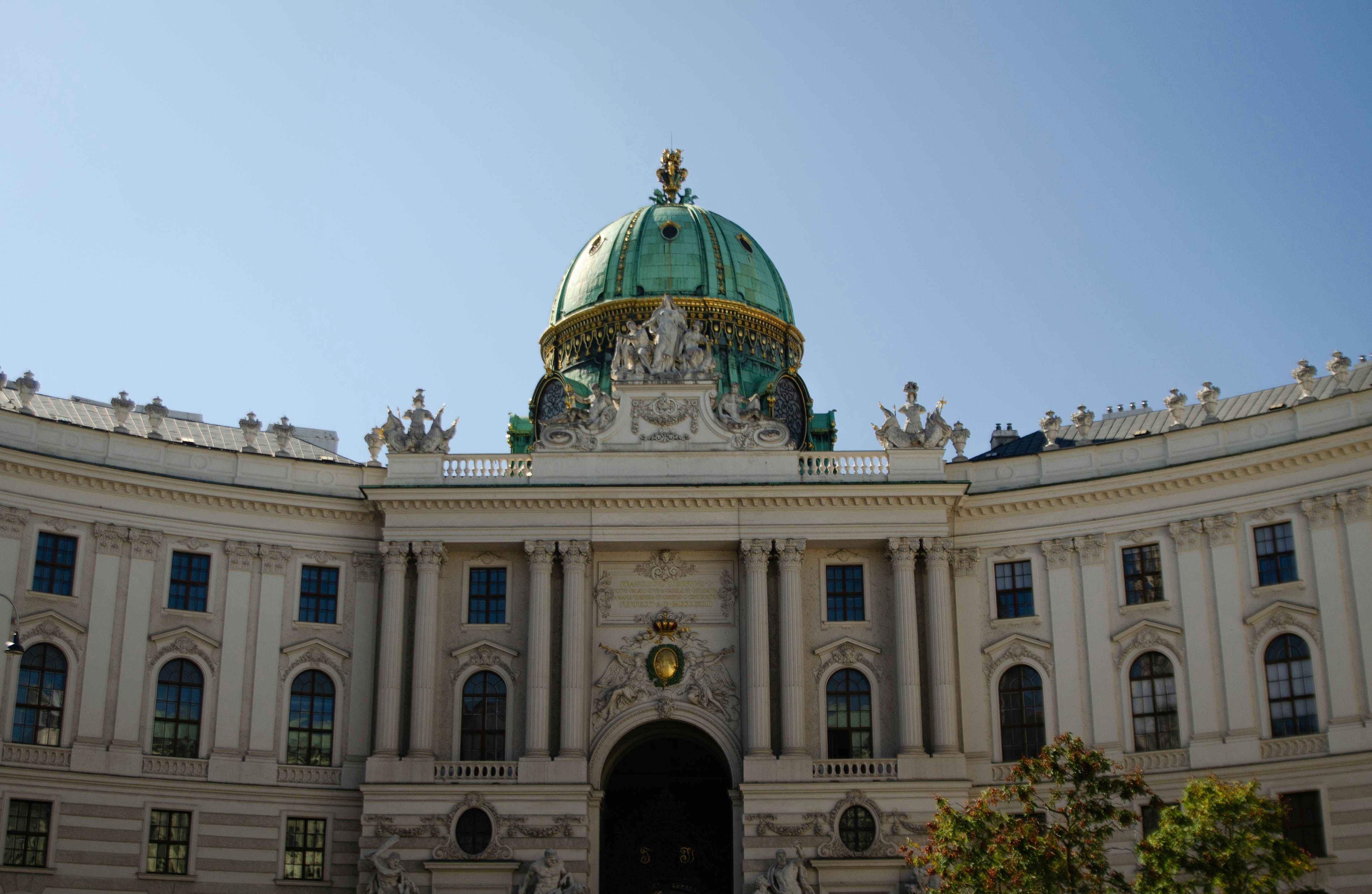 Imposing historical building with a striking green dome and intricate sculptures against a clear blue sky.