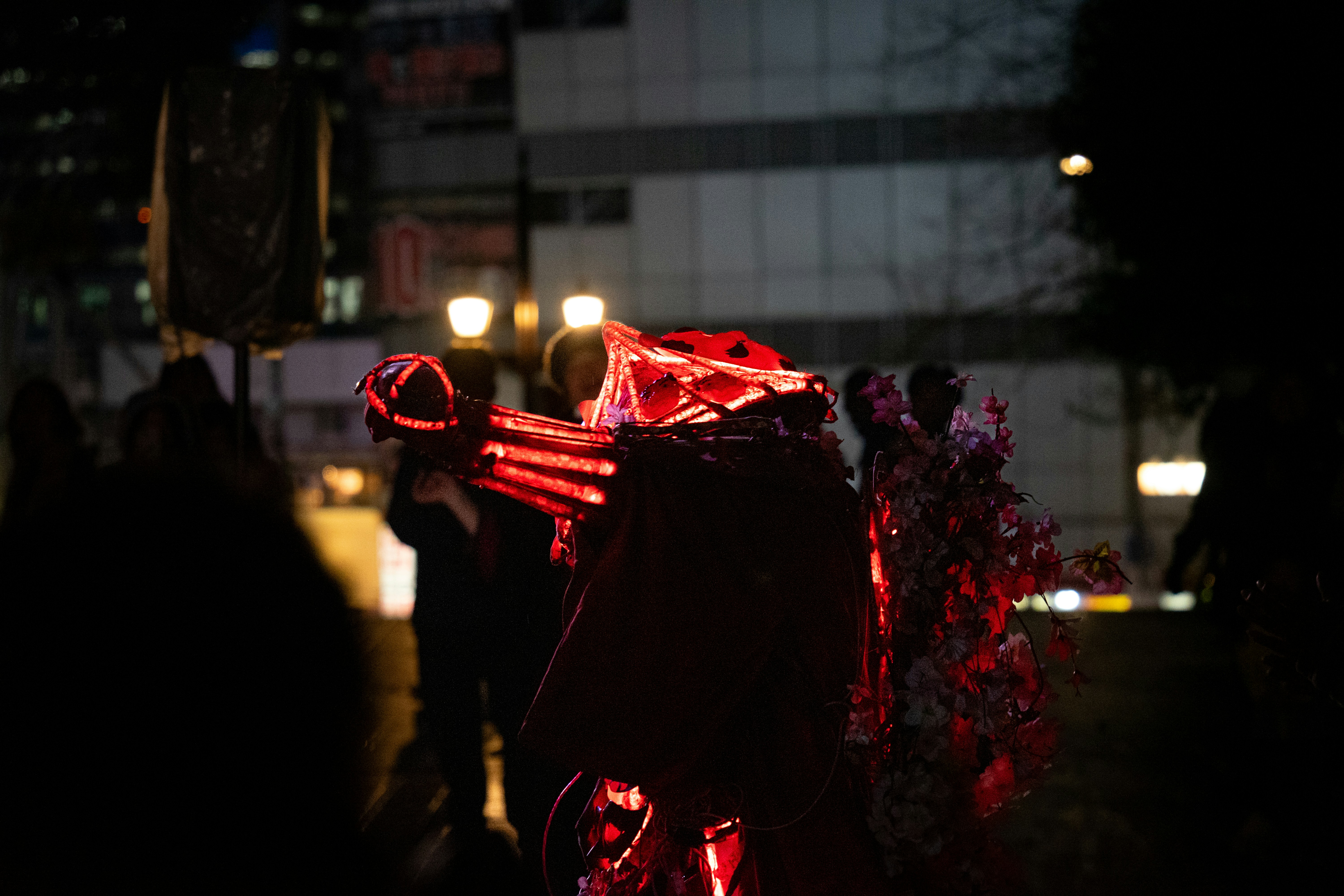 A photo of a dancer performing during a Hanami event in Ueno Park, Tokyo. | People in costumes with glowing red lights at night.