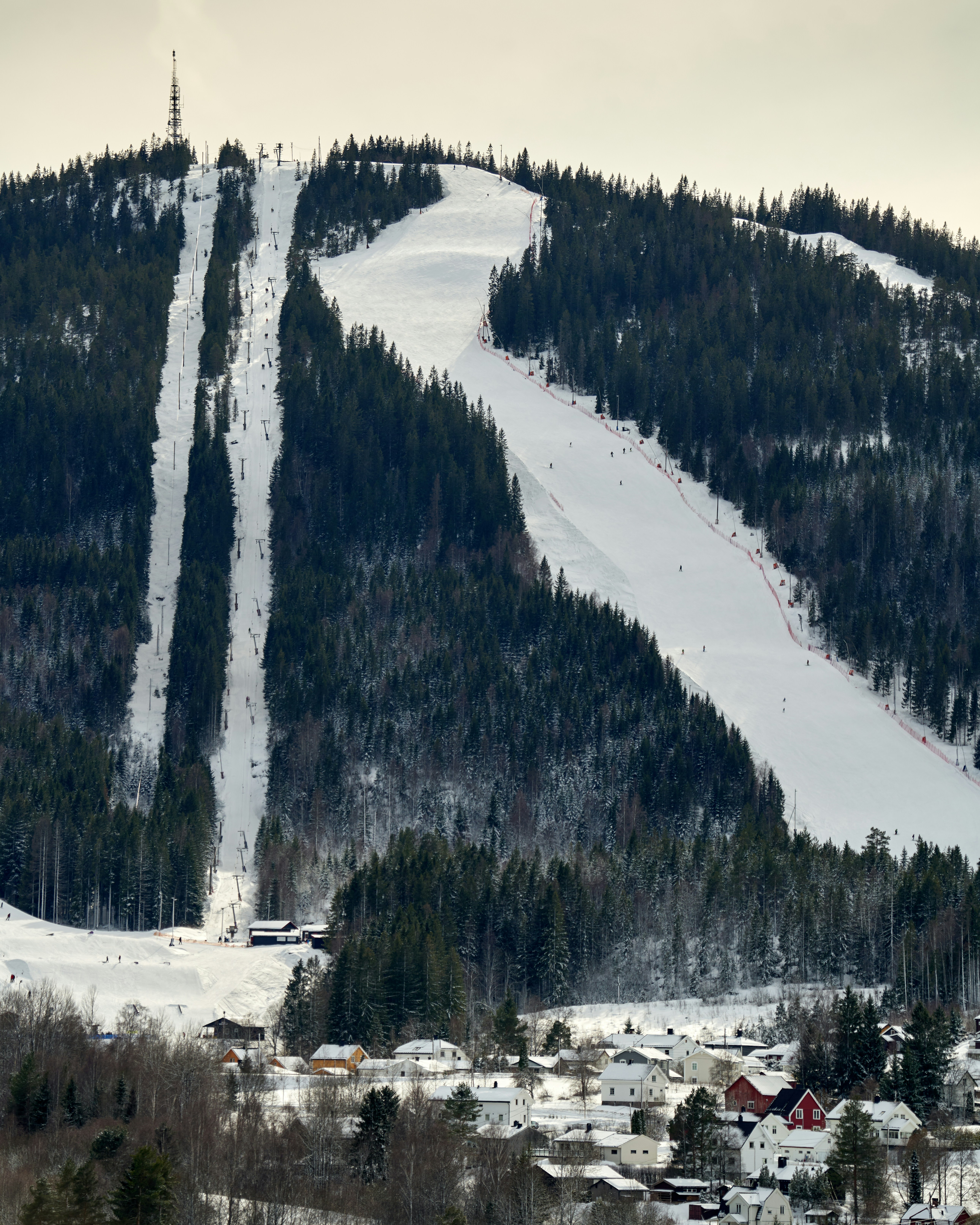 Snow-covered ski slopes descend from a forested mountain, with a small village nestled at the base. A ski lift and trails are visible, showcasing winter sports activity.