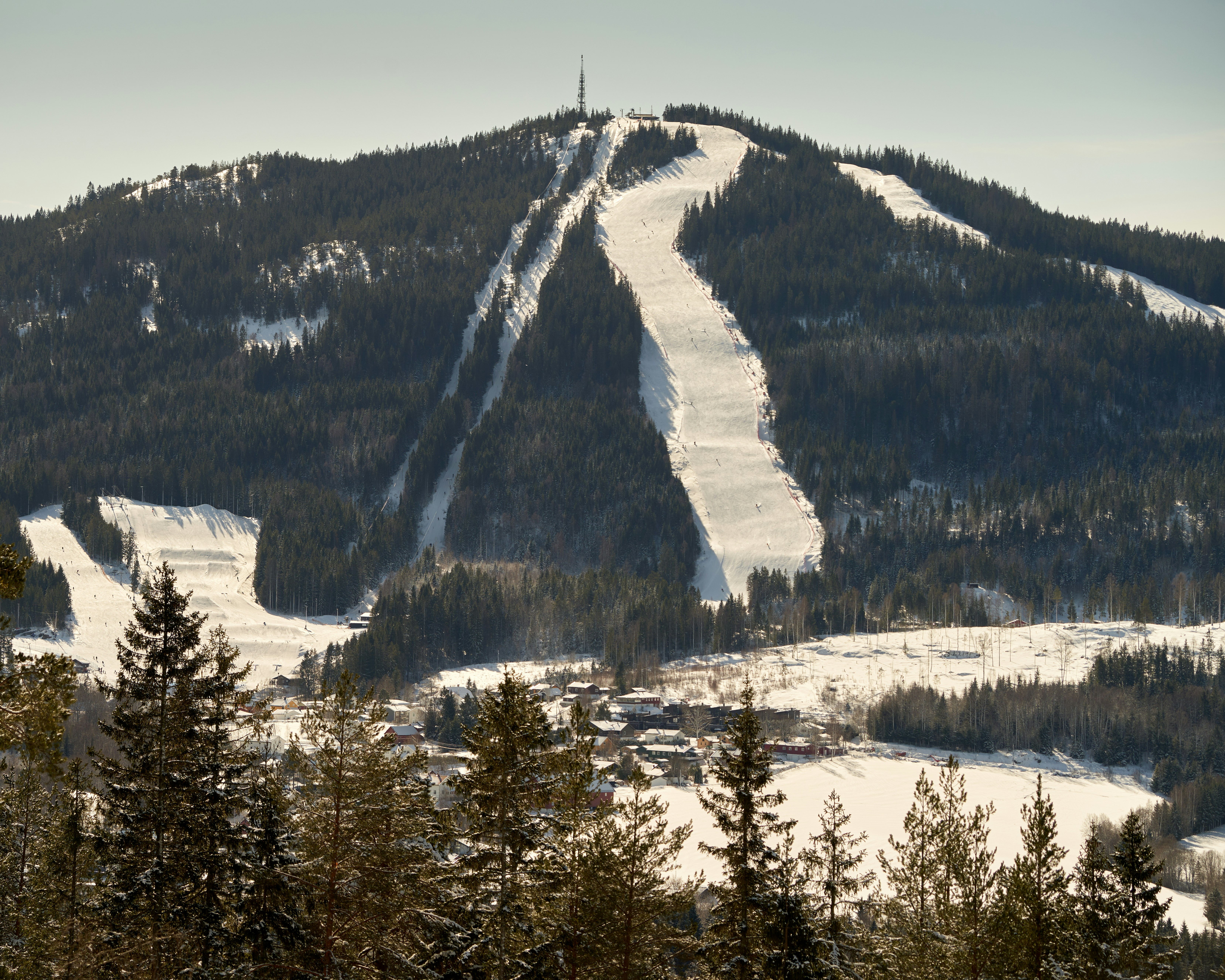 Small slalom ski center next to a small village with a lift and a downhill run north of Oslo, with skiers in winter | Snowy mountain with ski slopes and forest
