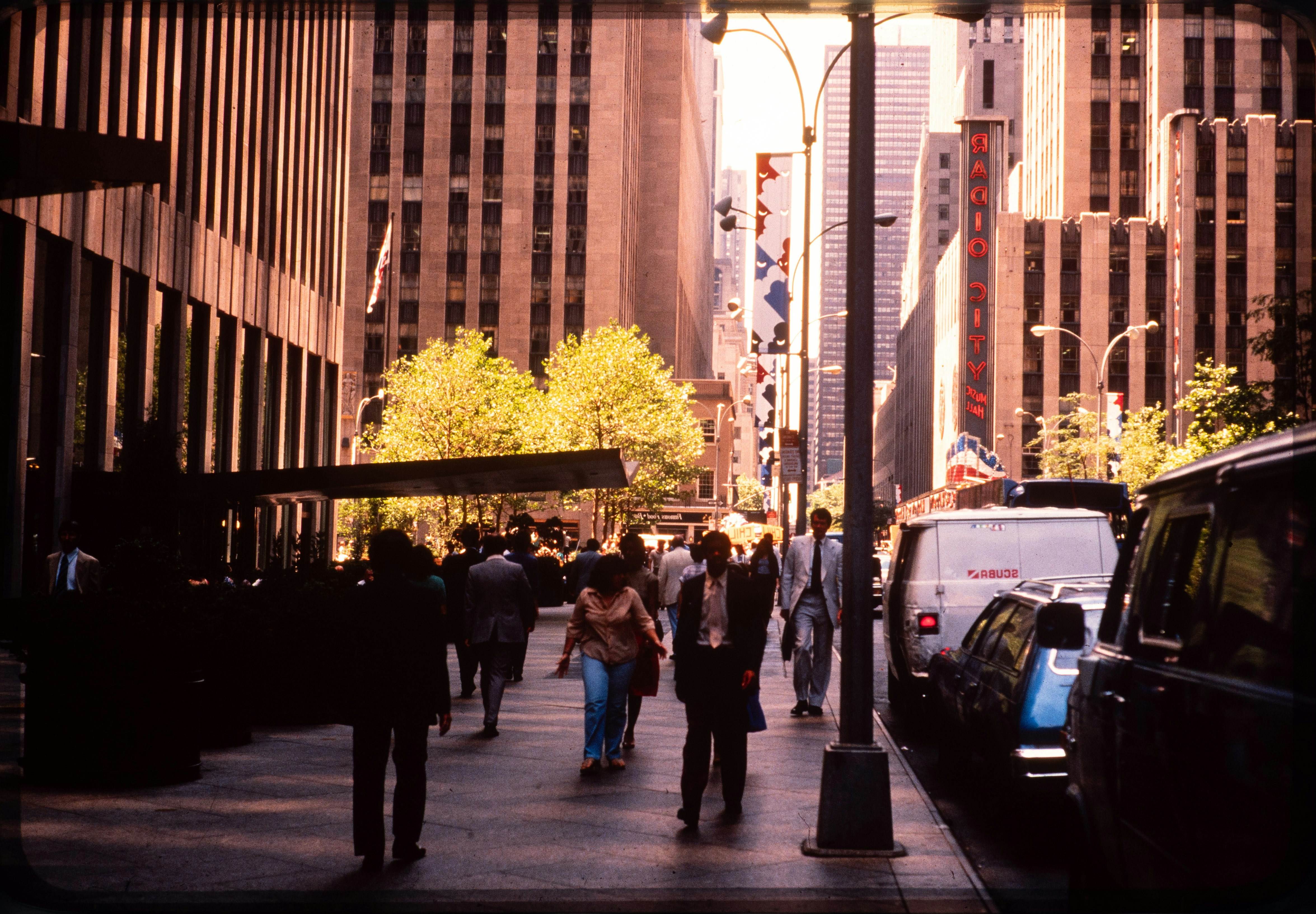 OLYMPUS DIGITAL CAMERA | People walk on a sunny city sidewalk with buildings.
