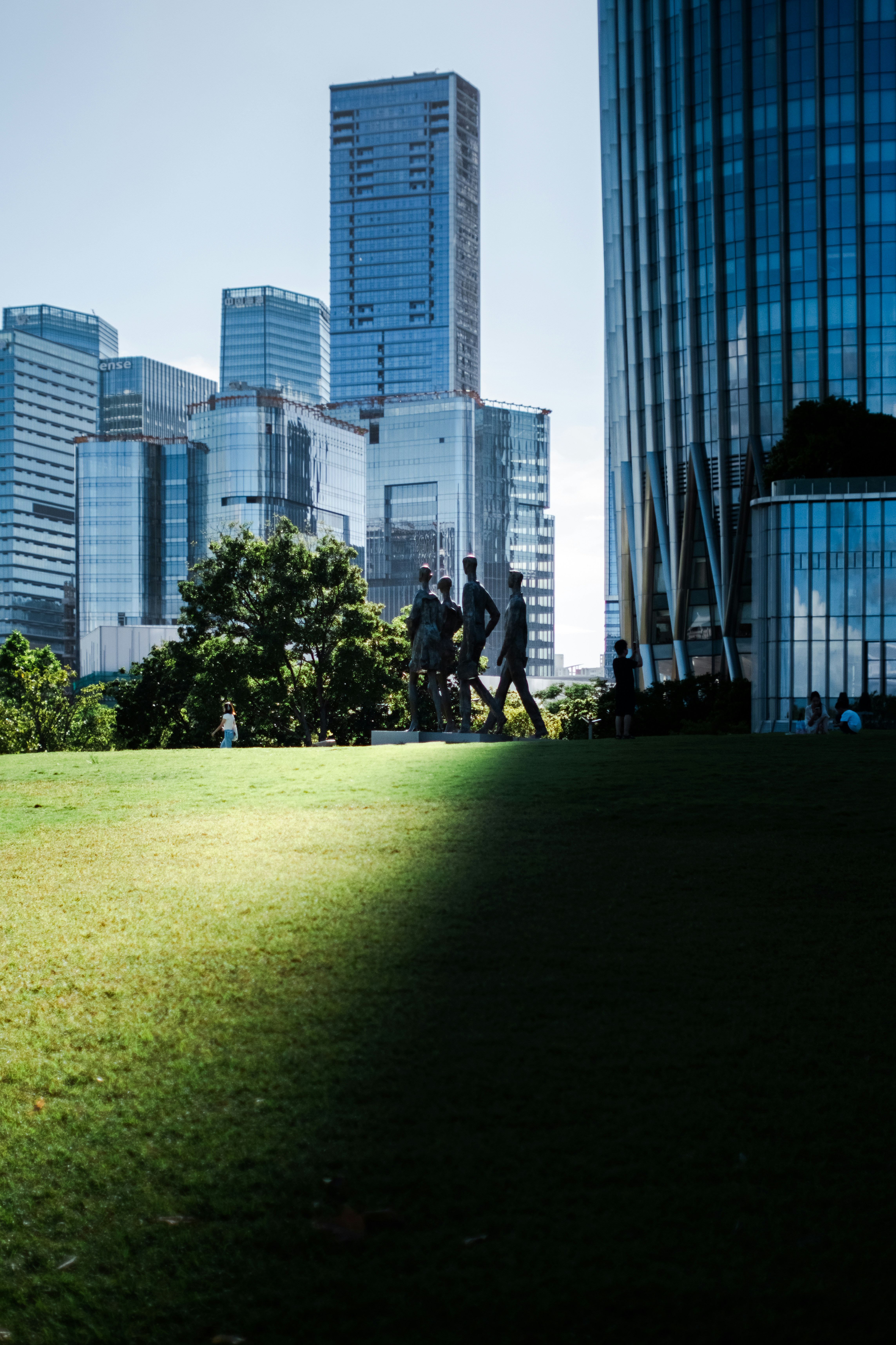 Silhouetted figures walk across a grassy hill with skyscrapers.
